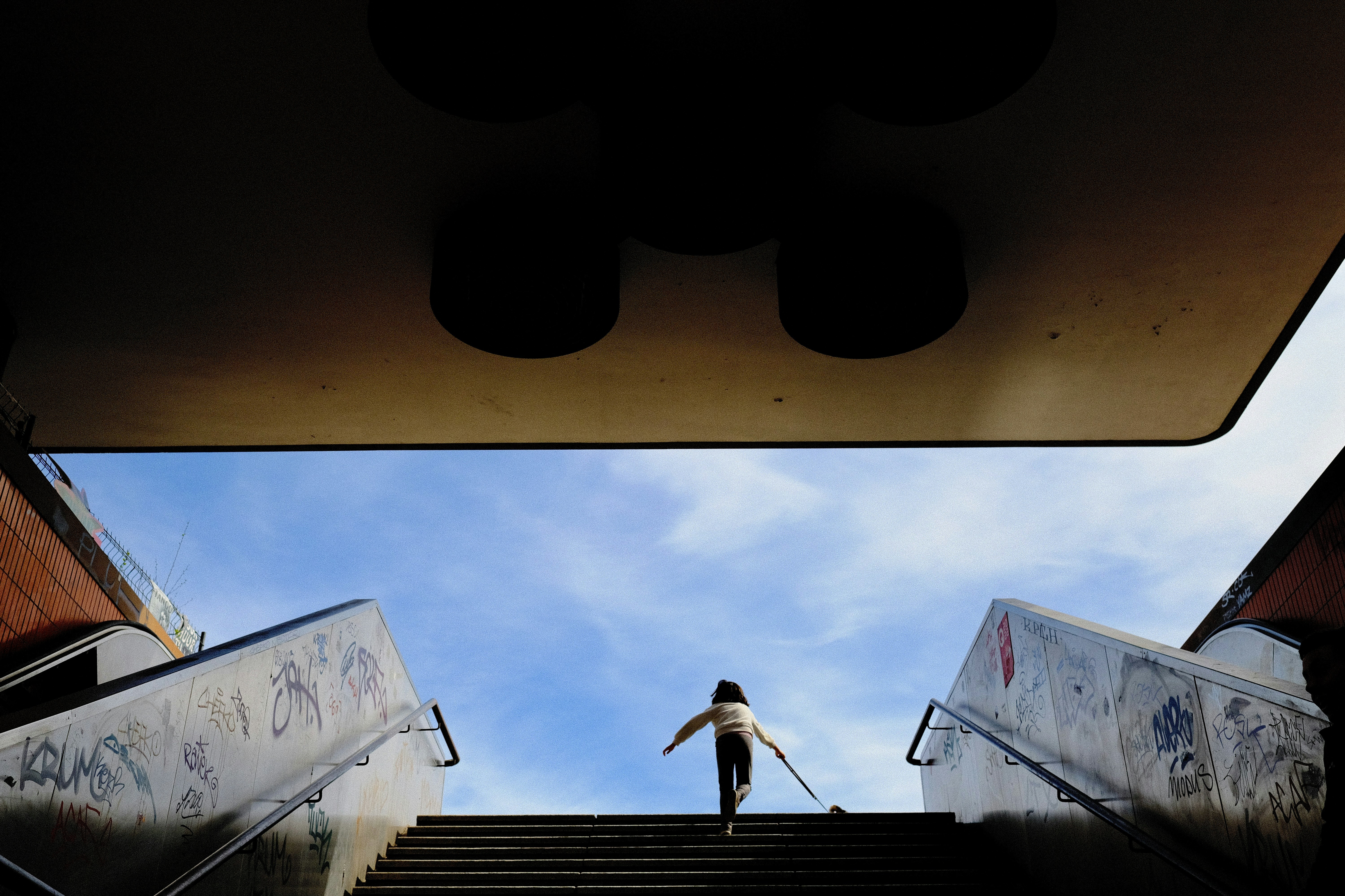 Mid-Flight Ascent: A lone figure descending the stairway toward the open sky
