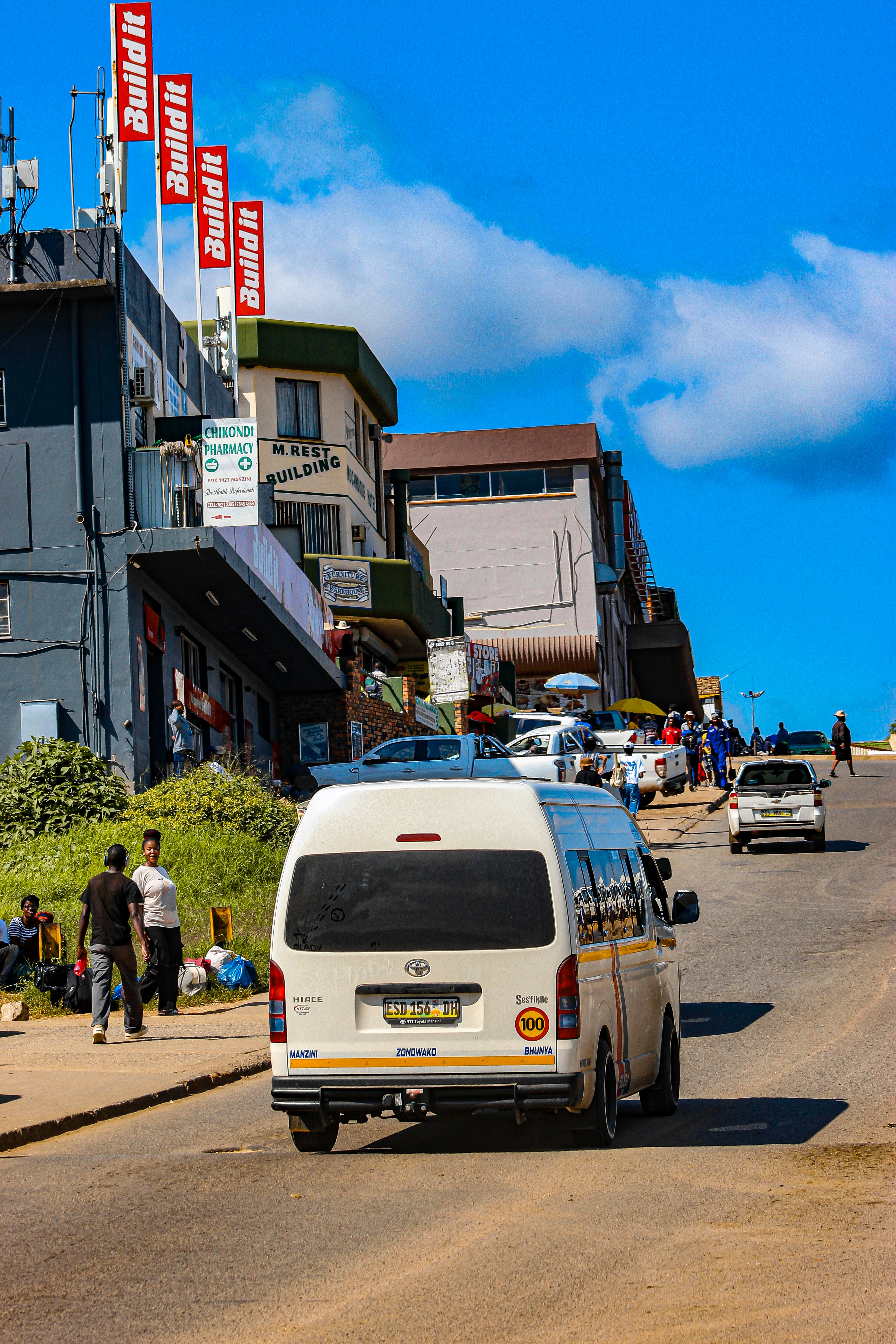 Street ascend: a white van leads a market-slung ascent under a row of red banners