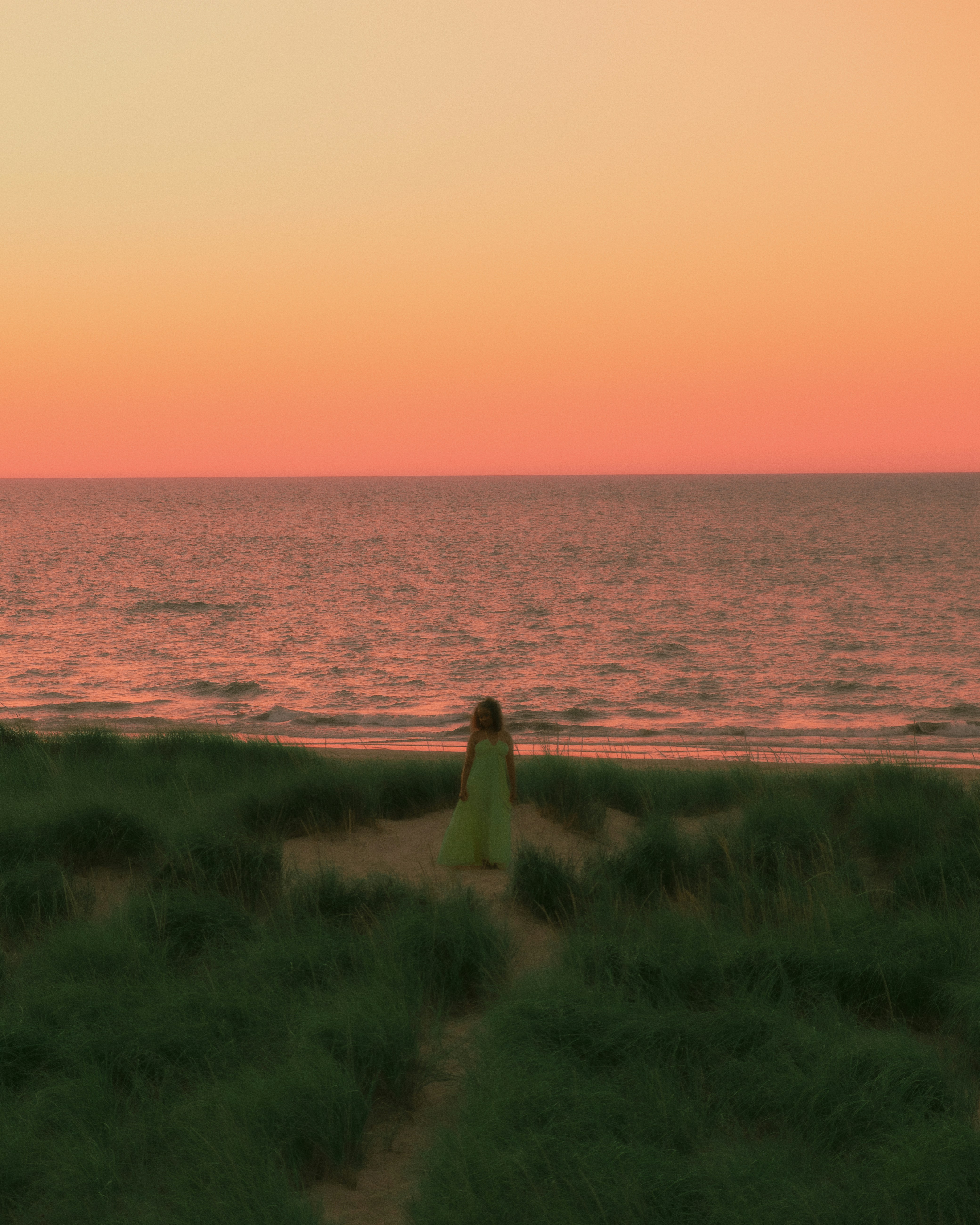 Woman in green dress walking on beach at sunset