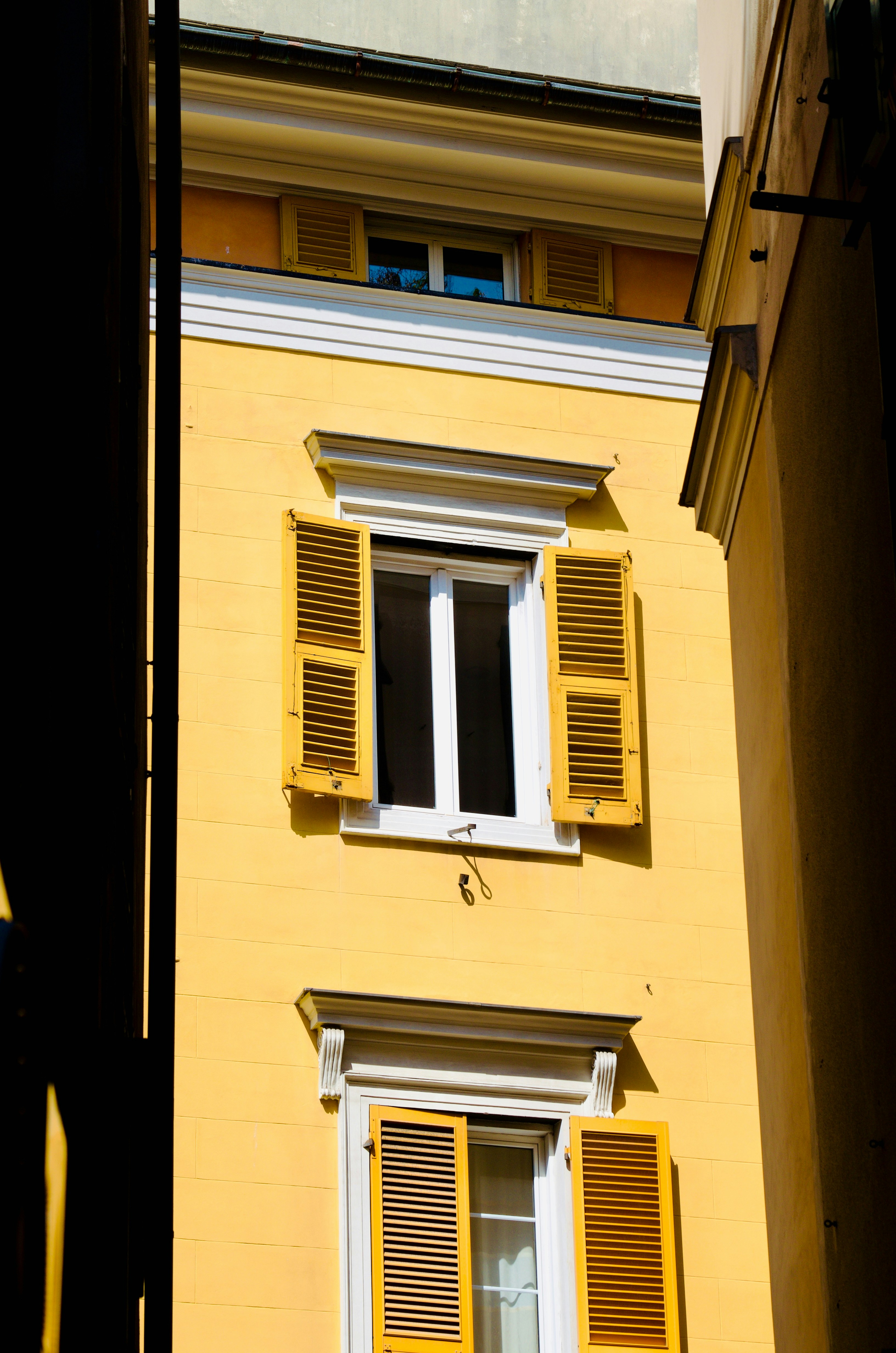 Sunlit Yellow Facade with Open Window Shutters