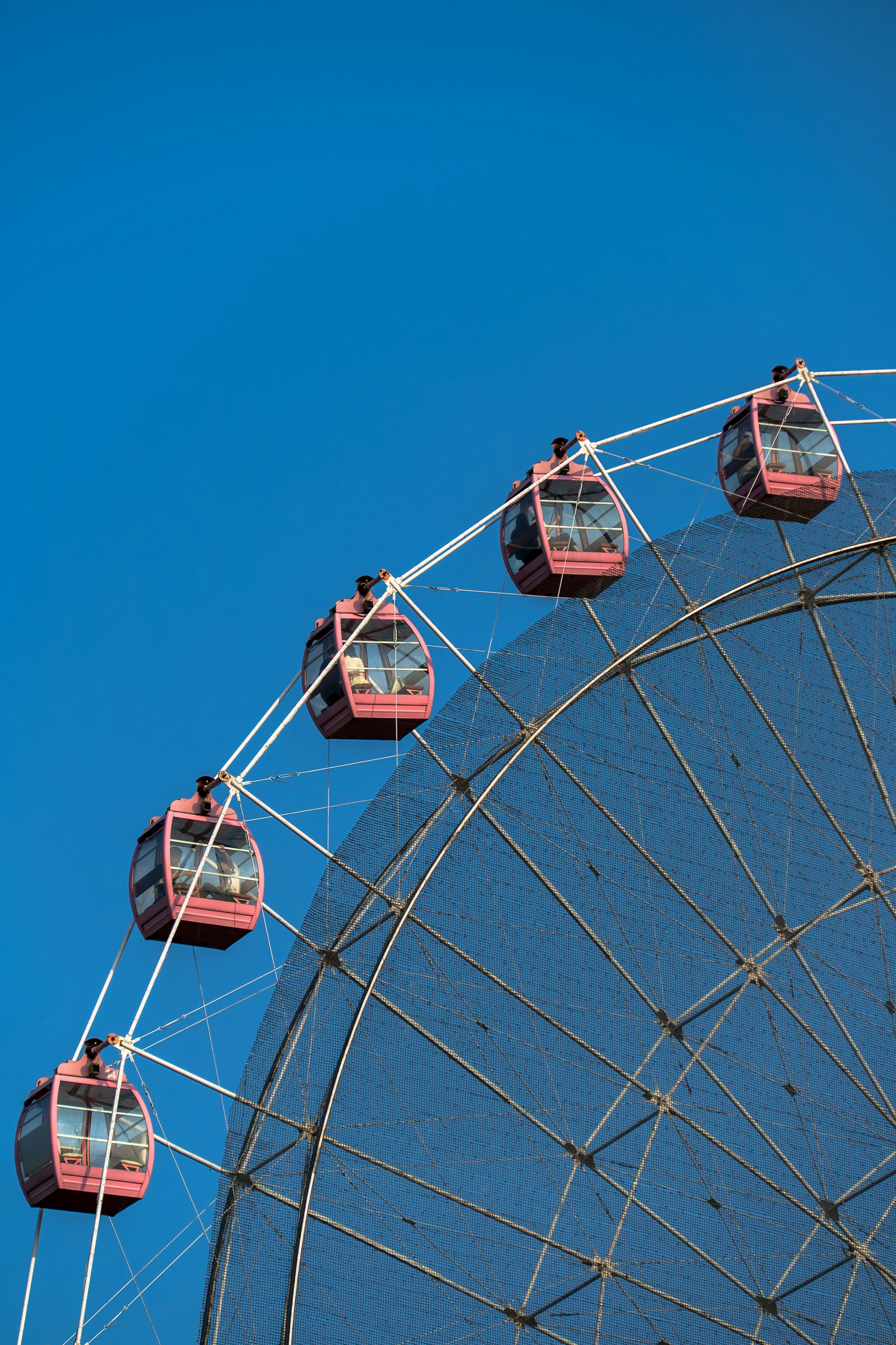 Pink gondolas sail the blue sky along a Ferris wheel arc