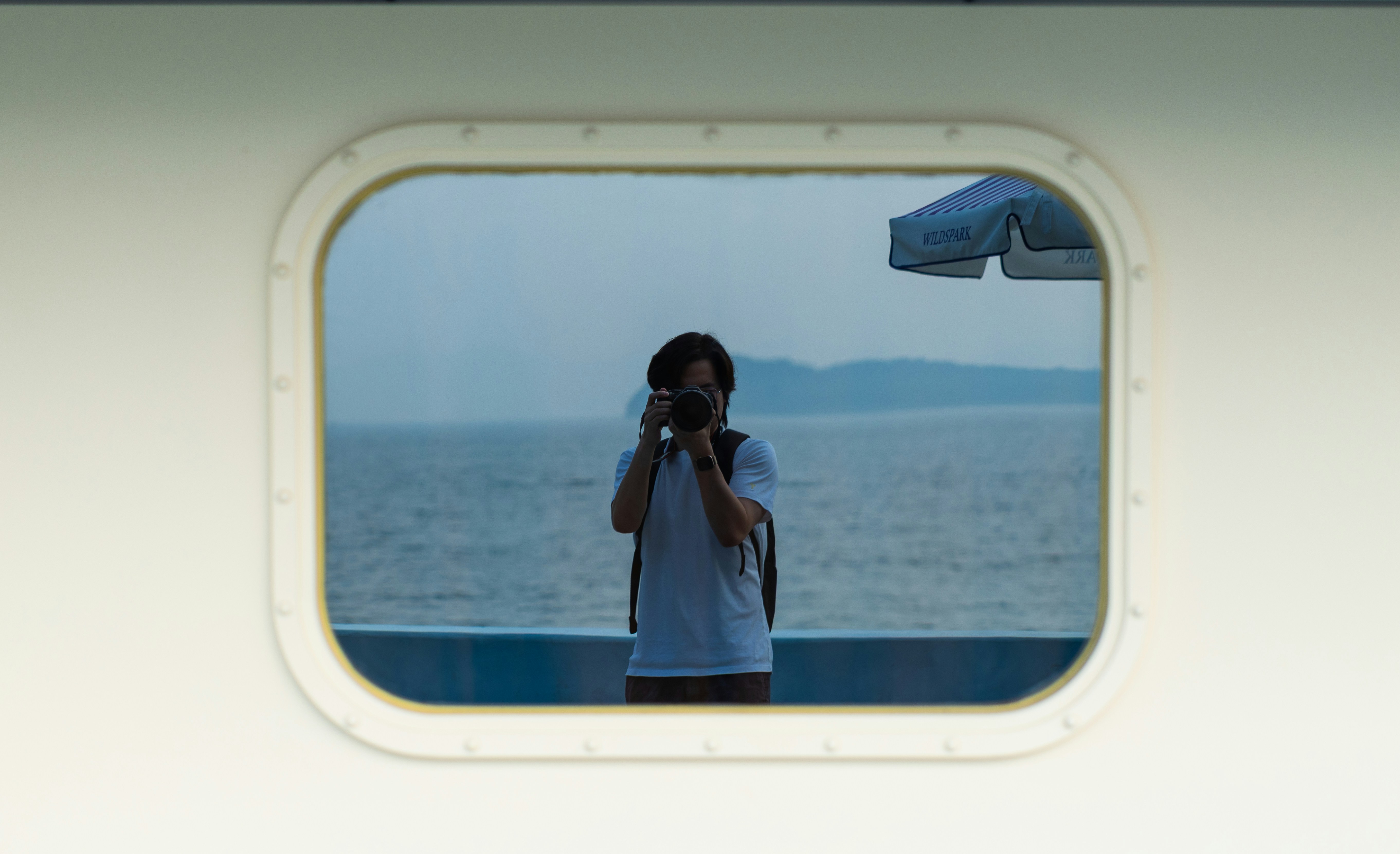 Portrait in a Porthole: A Photographer Framed by Sea and Window