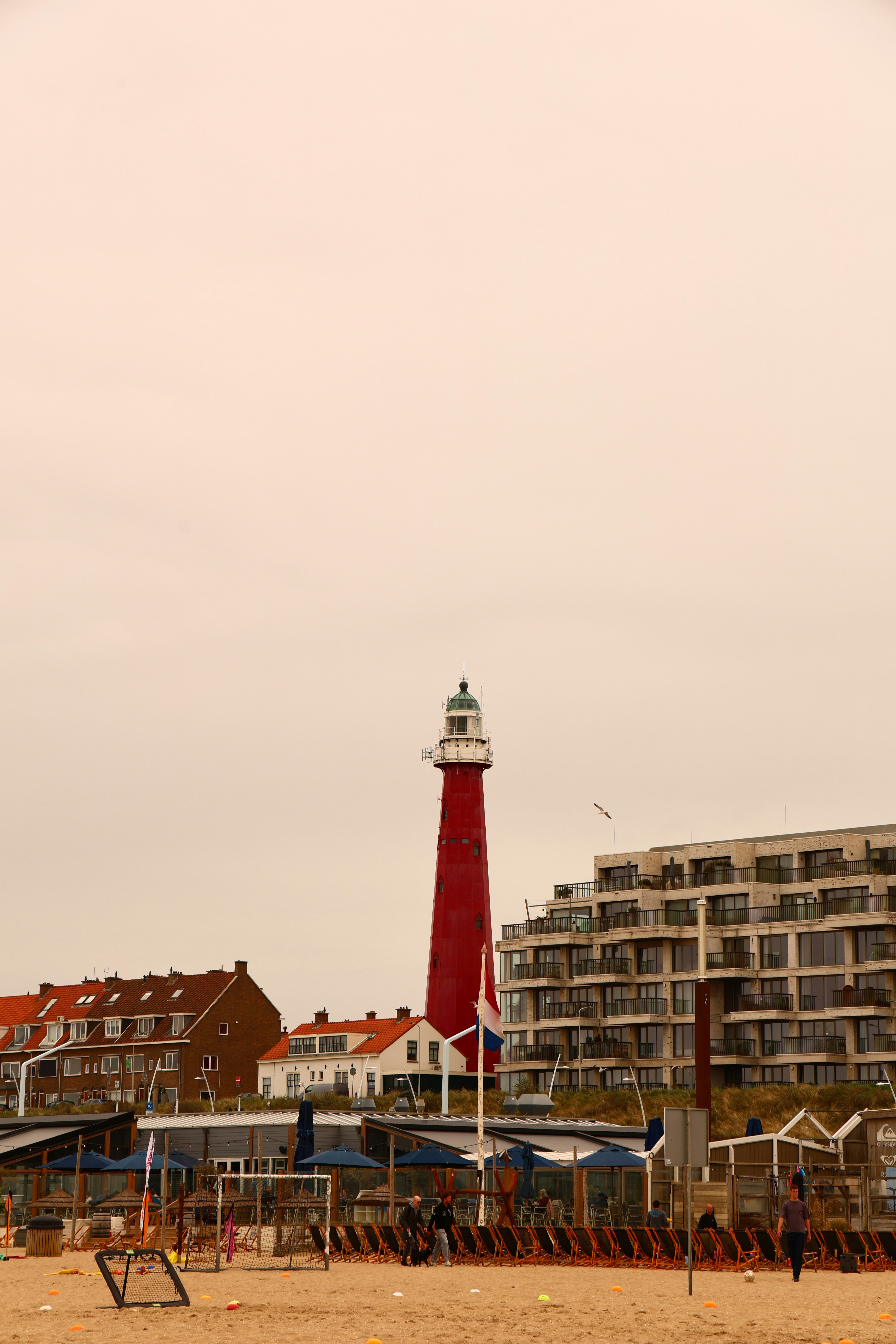 Red lighthouse stands beside buildings on beach