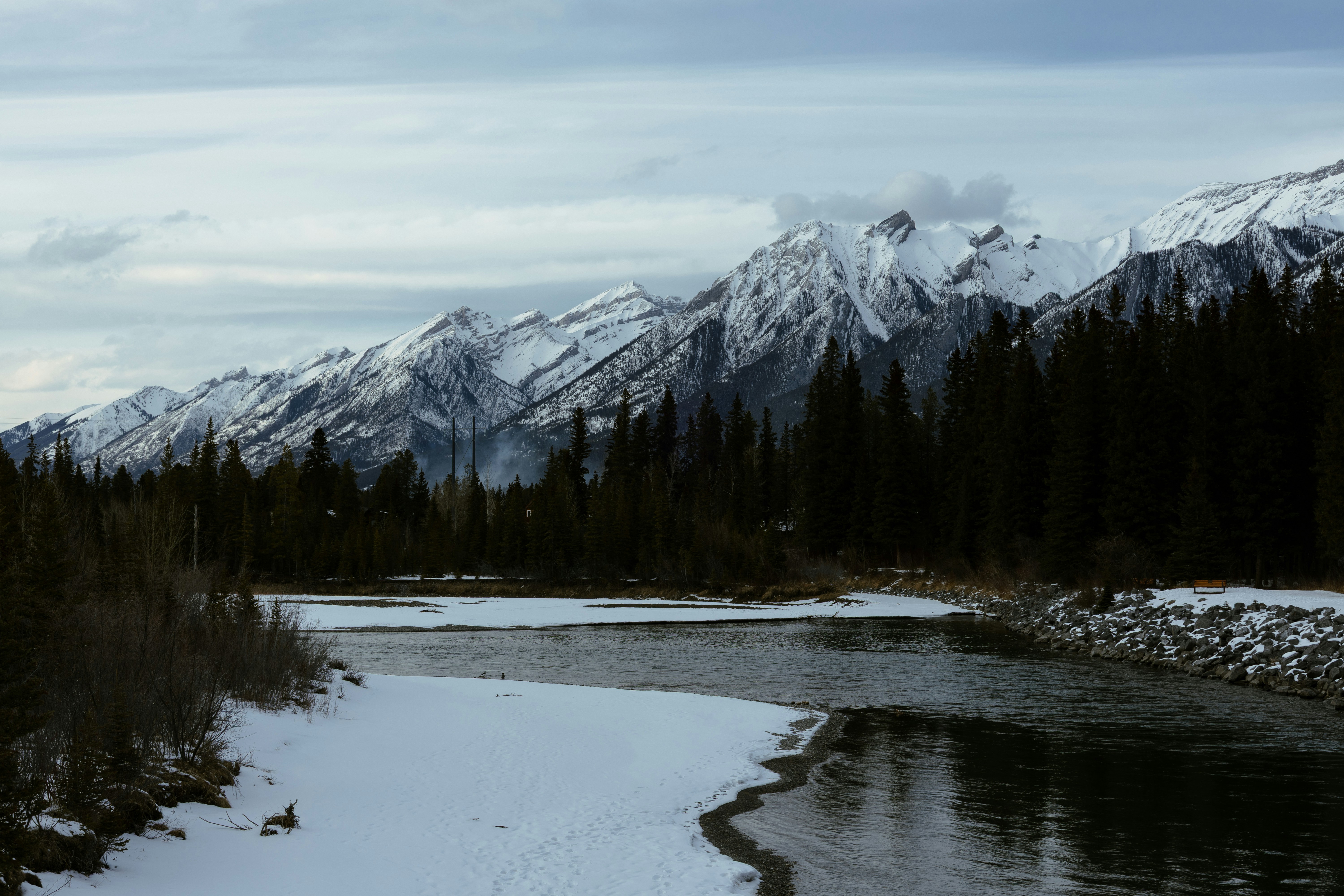 Snowy mountains overlook a frozen river and dark forest.