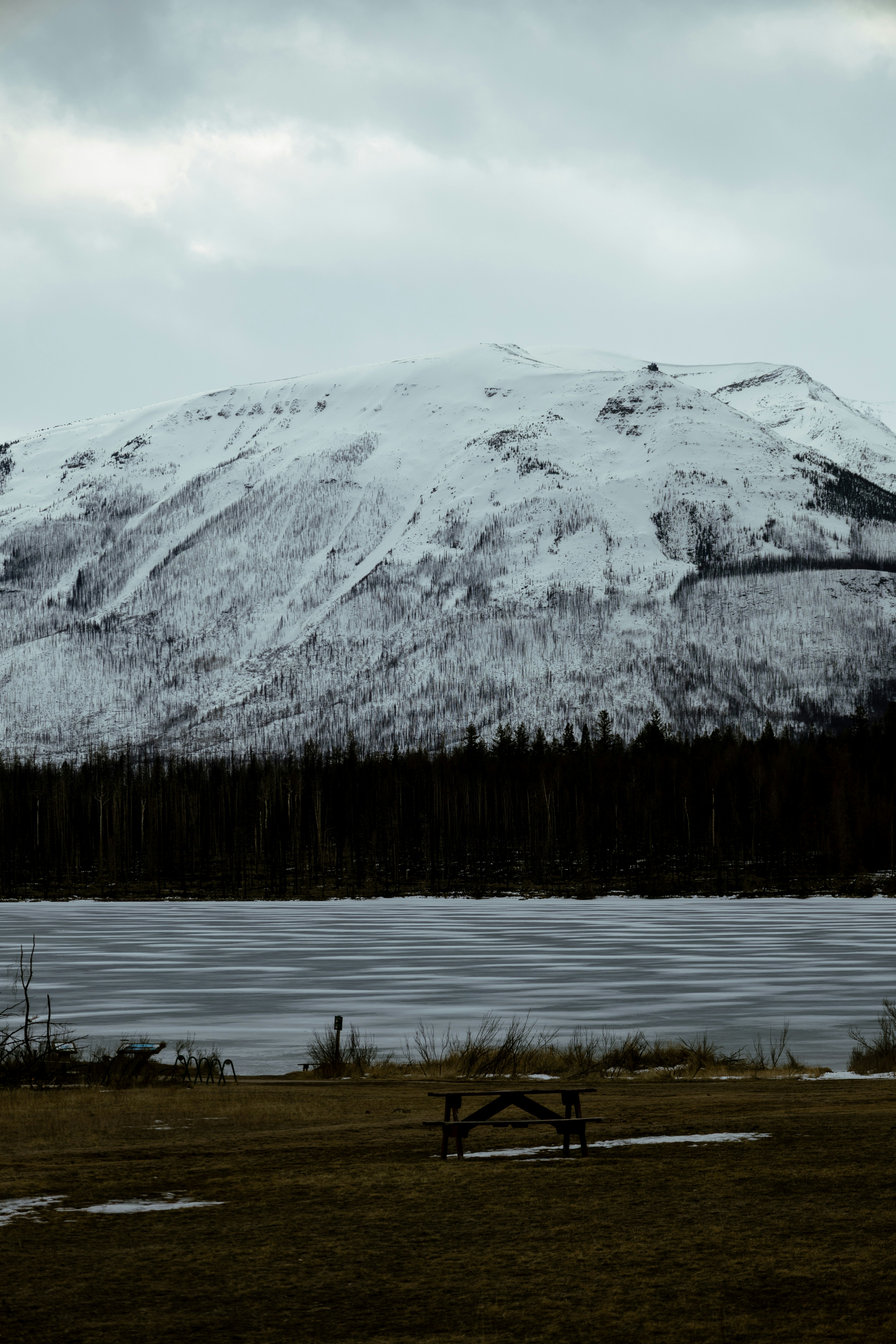 Snow-dusted ridge over still lake with a lone picnic table