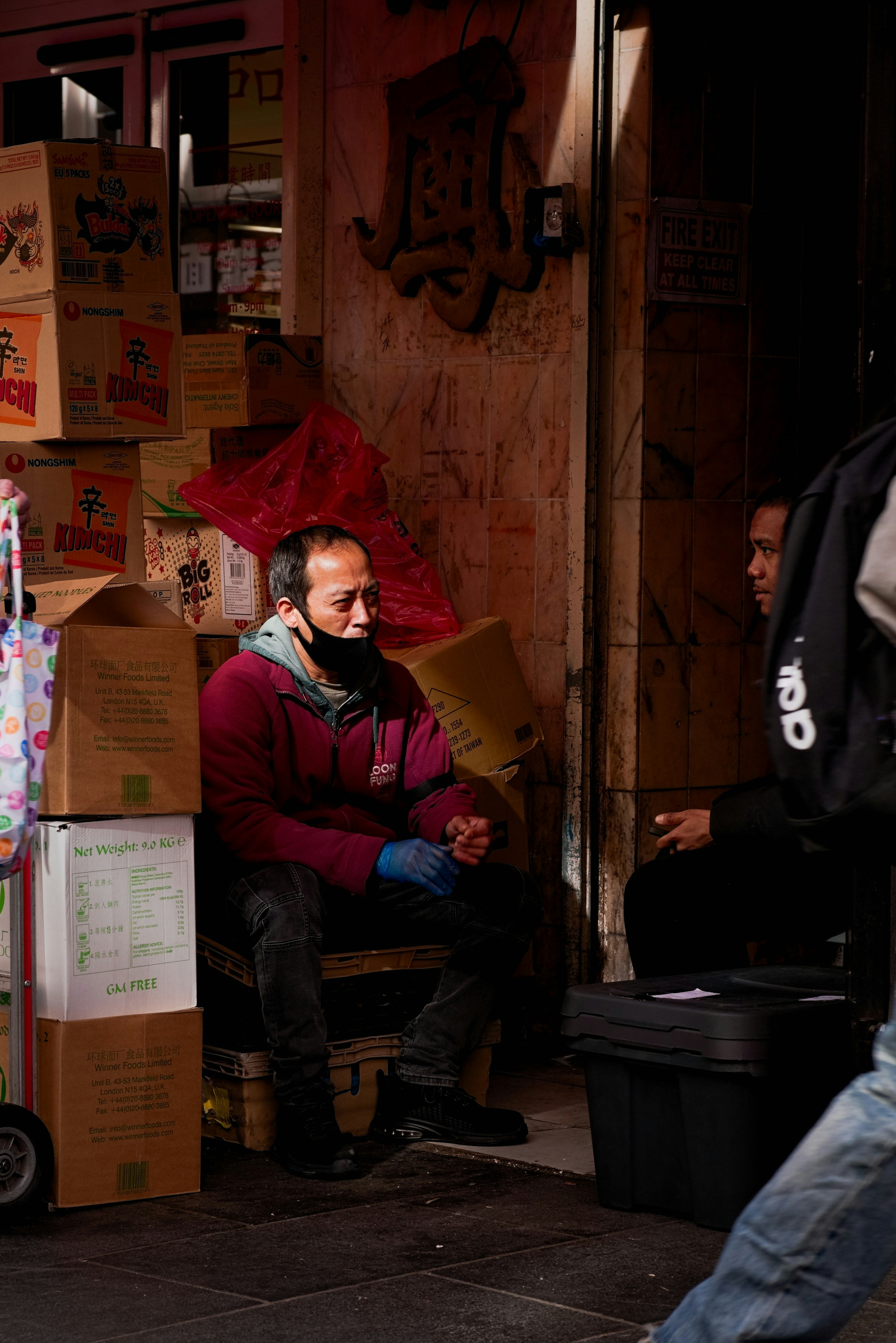 Street Market Silence: A Worker in the Shadows of Cardboard Pallets