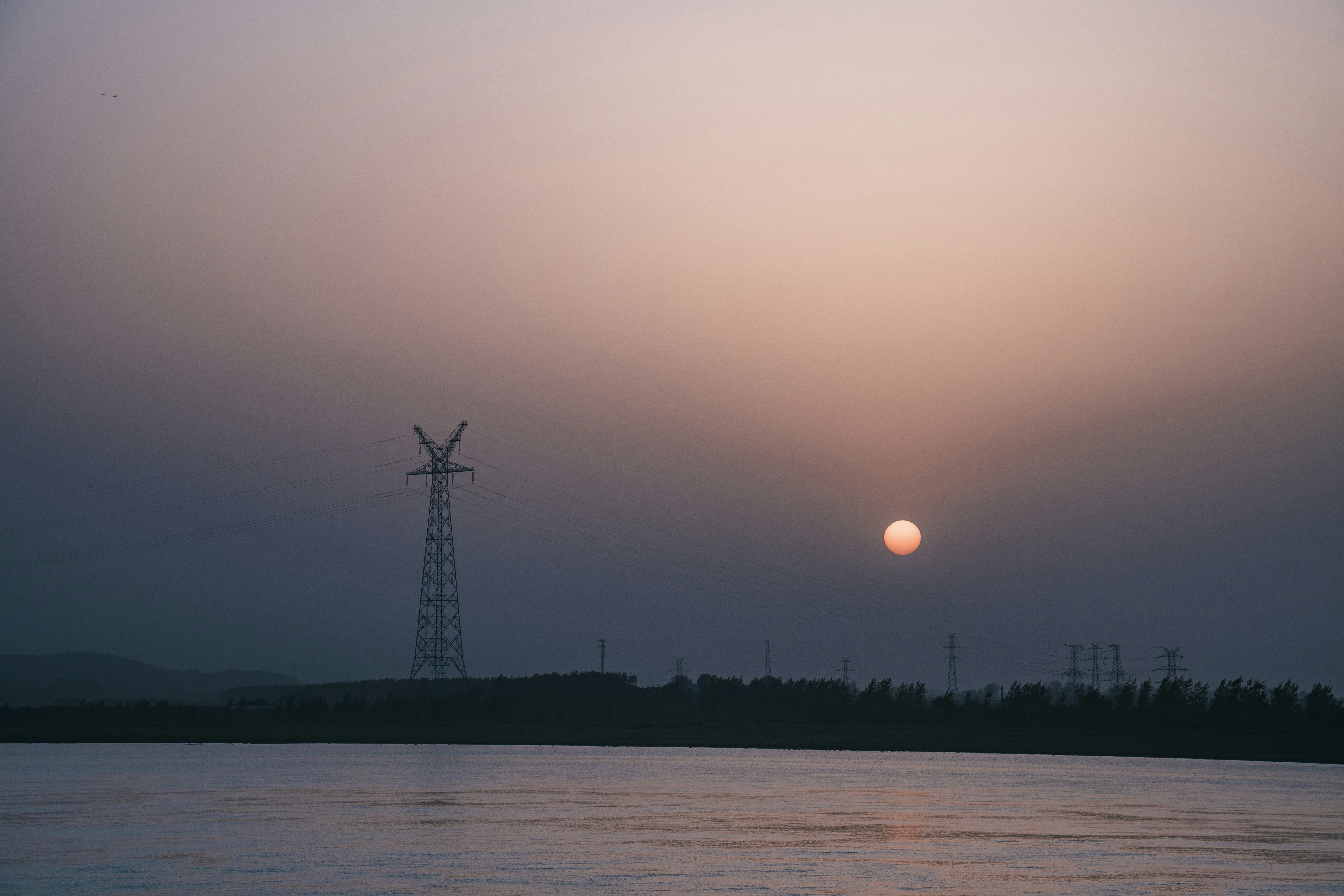 Horizon of quiet power: sun sinking beside a lattice of transmission towers