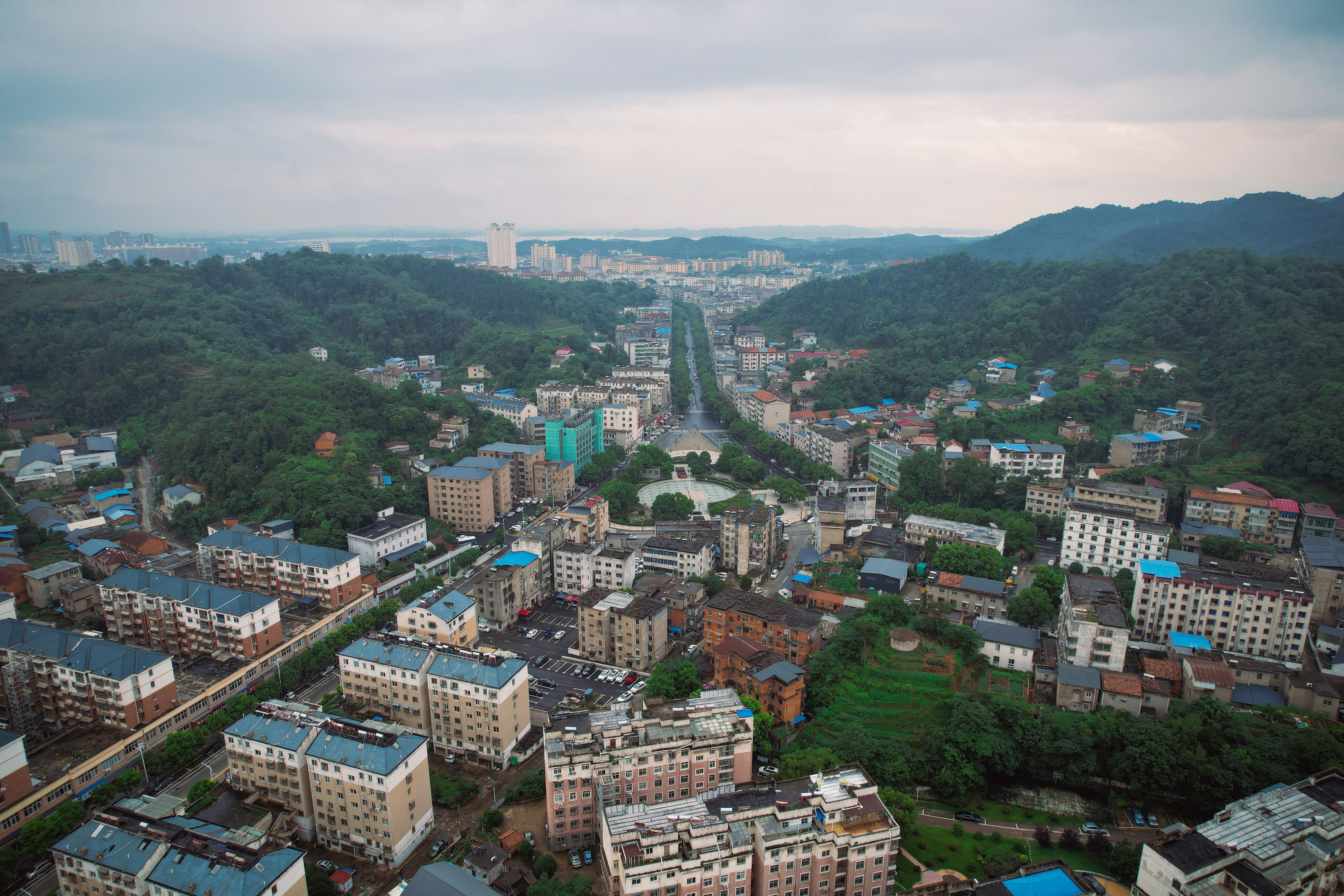 Aerial Ribbon: City Grid Wakes Between Green Hills