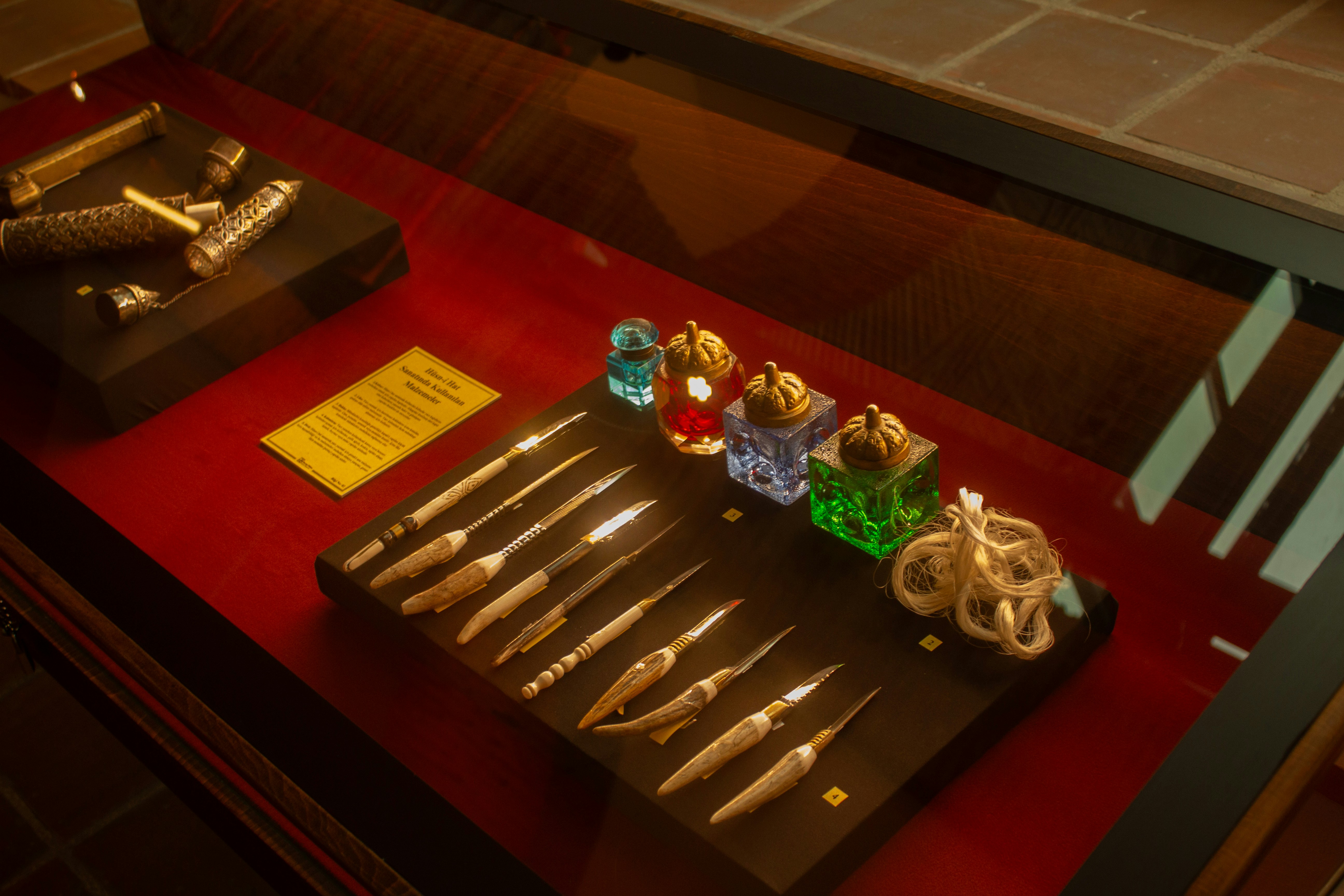 Miniature Carved Knives and Colorful Cylindrical Weights in a Red Display Case