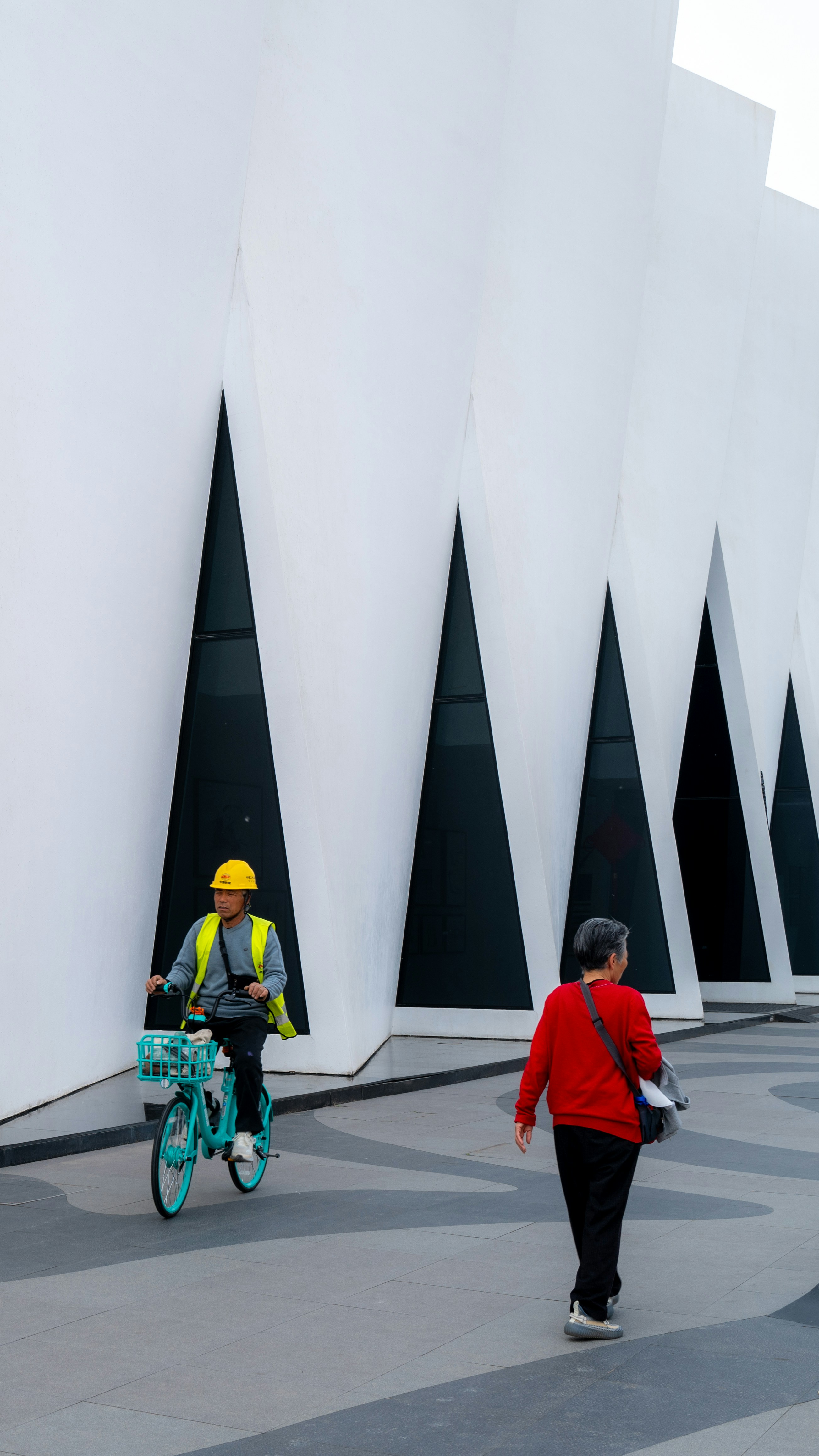 Contrasting Journeys: A Worker on a Turquoise Bicycle Passes a Geometric Facade
