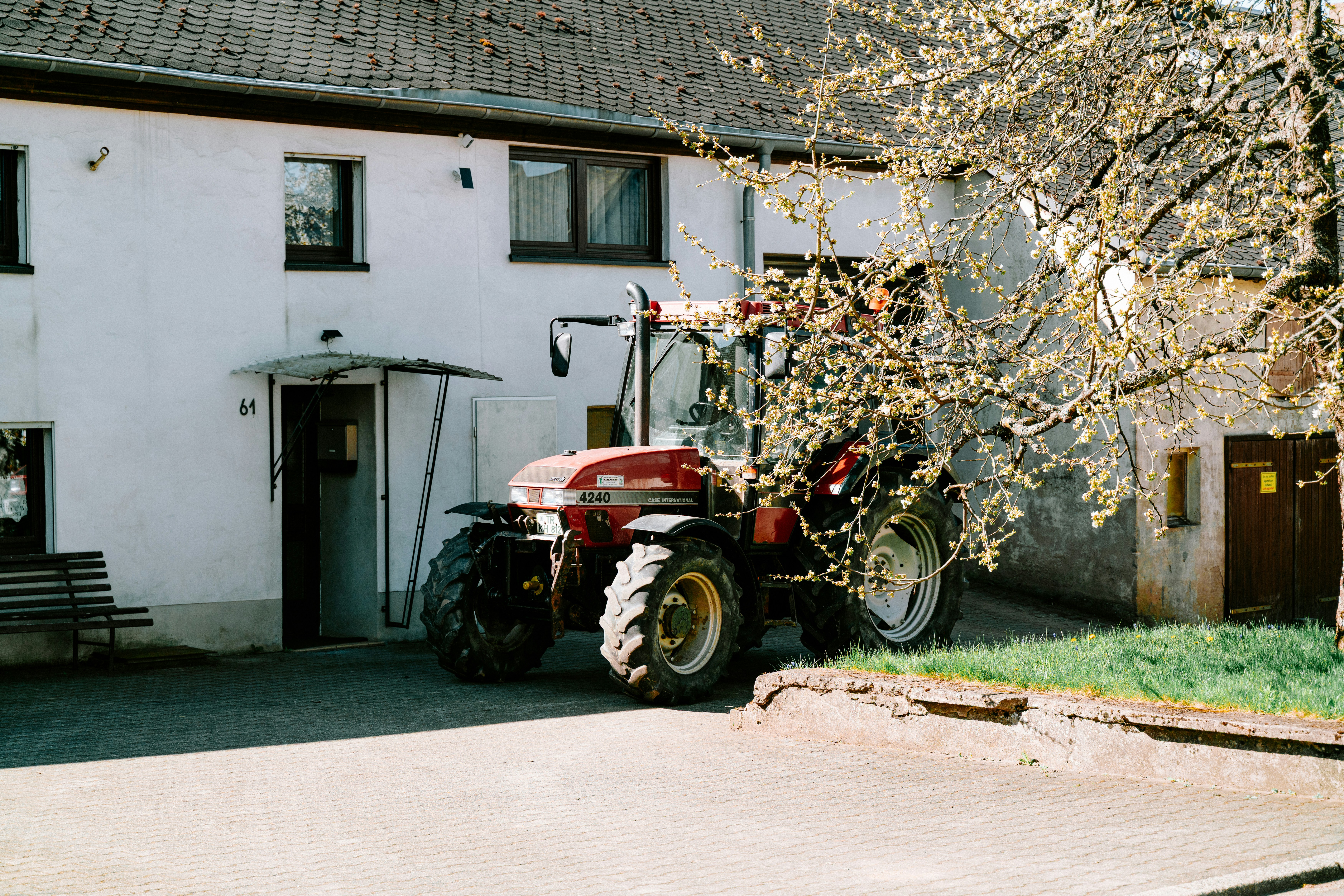 Dusty red tractor tucked beside a white-washed building