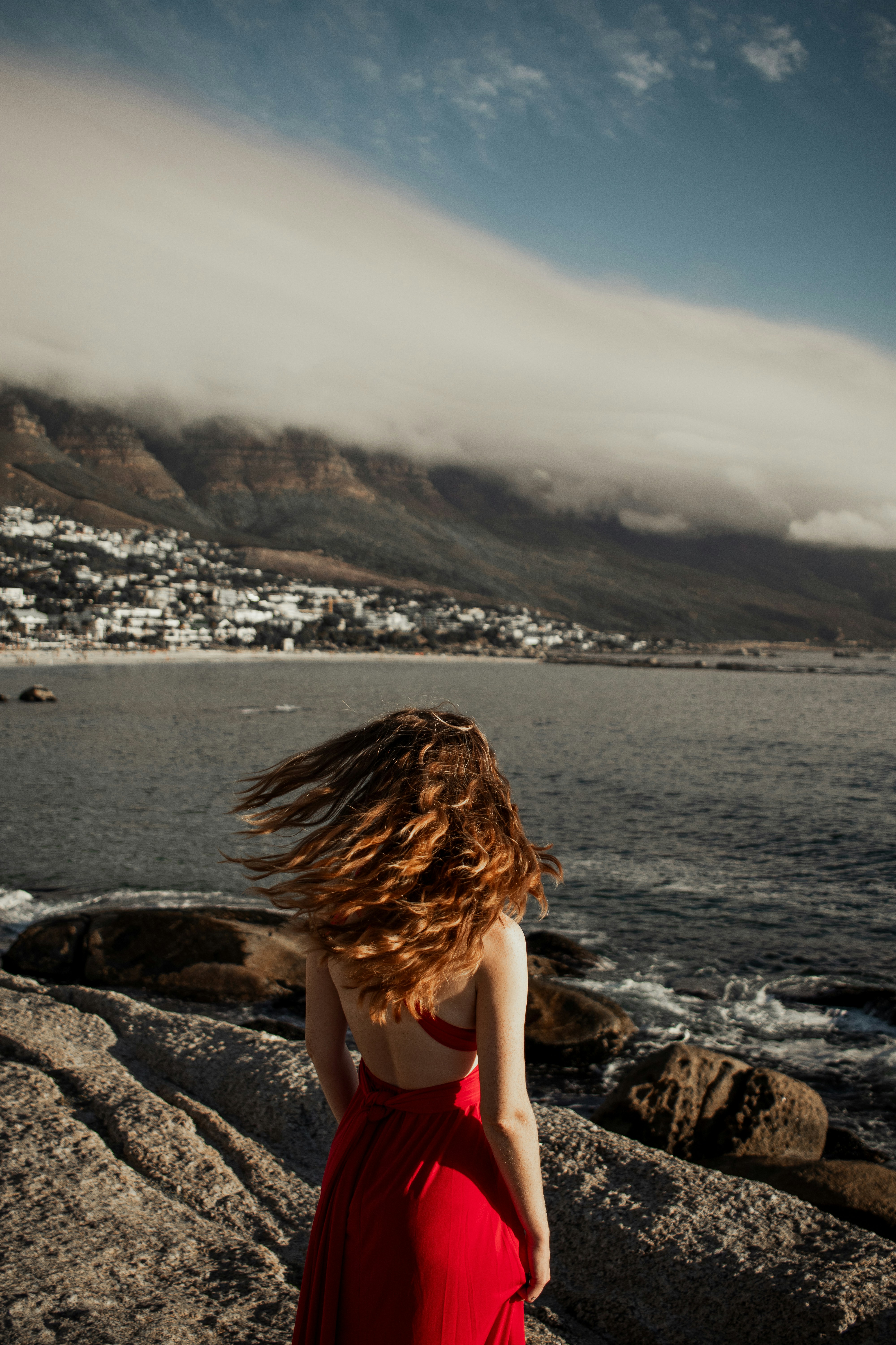 Red dress at the edge of sea-stone dunes beneath a cloud-topped panorama