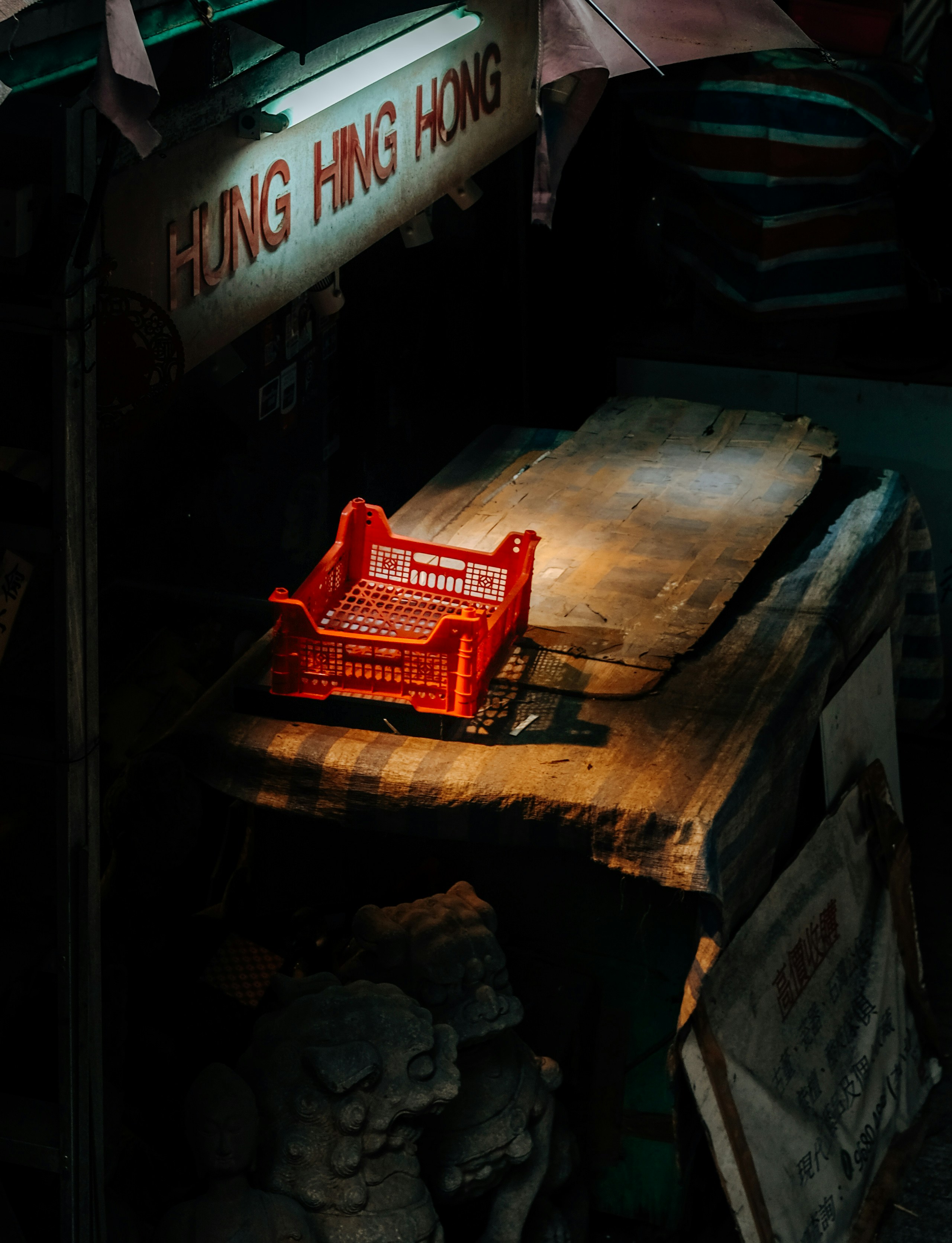 Red crate under green awning in dim market stall