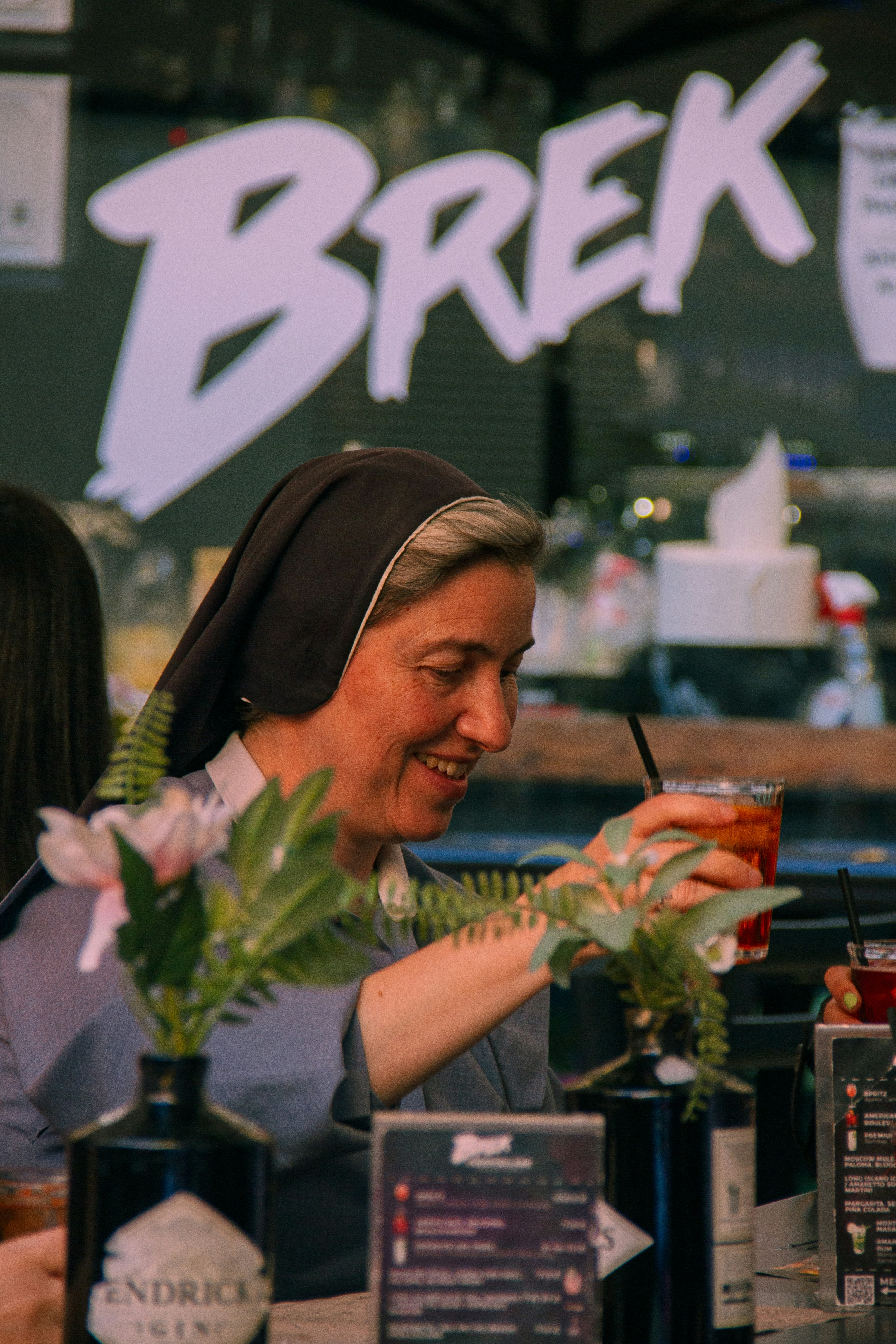 Smiling Nun toasting with a Scarlet Drink at a Café Bar