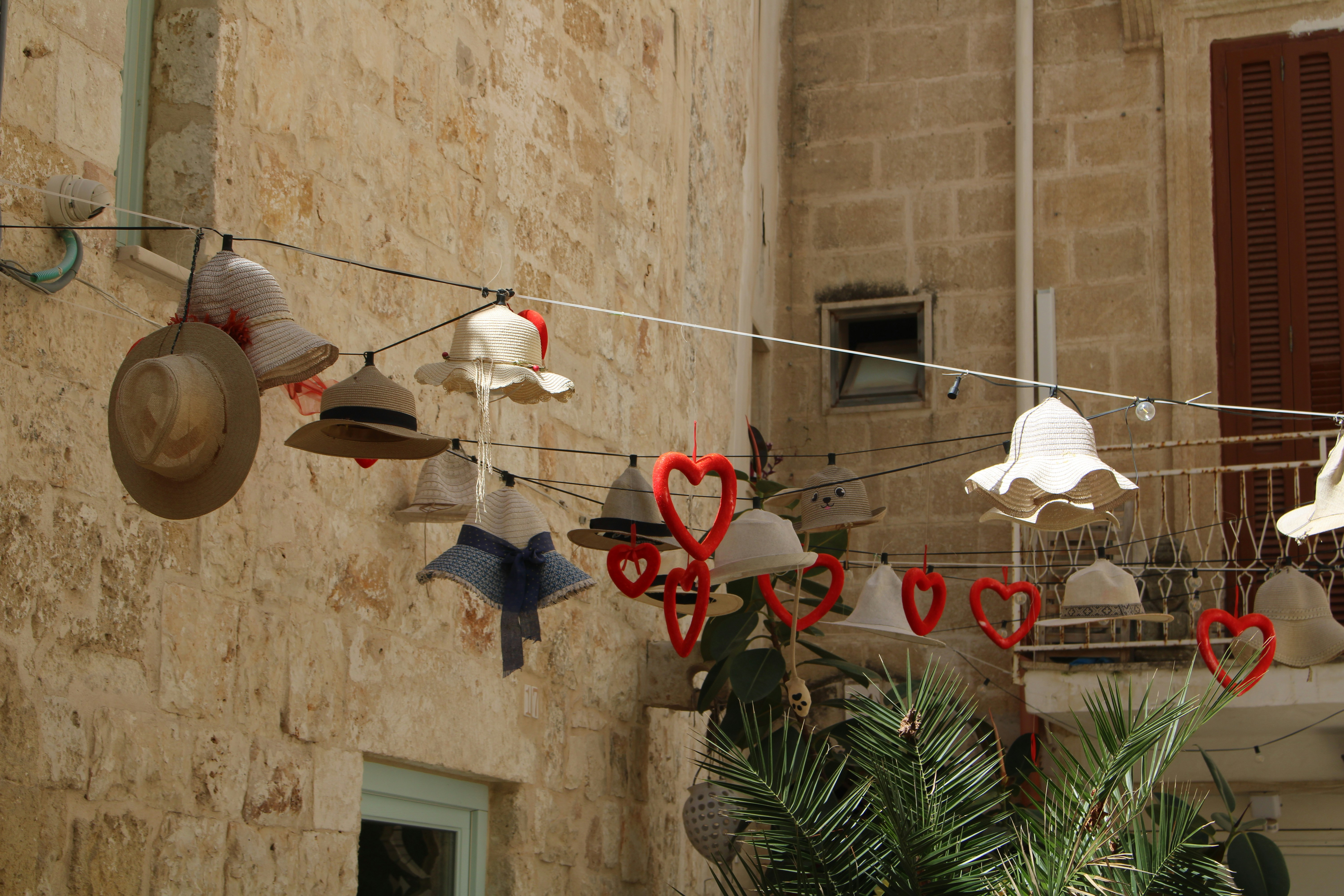 Sunny Street Bazaar: Hats and Hearts on a Stone Facade