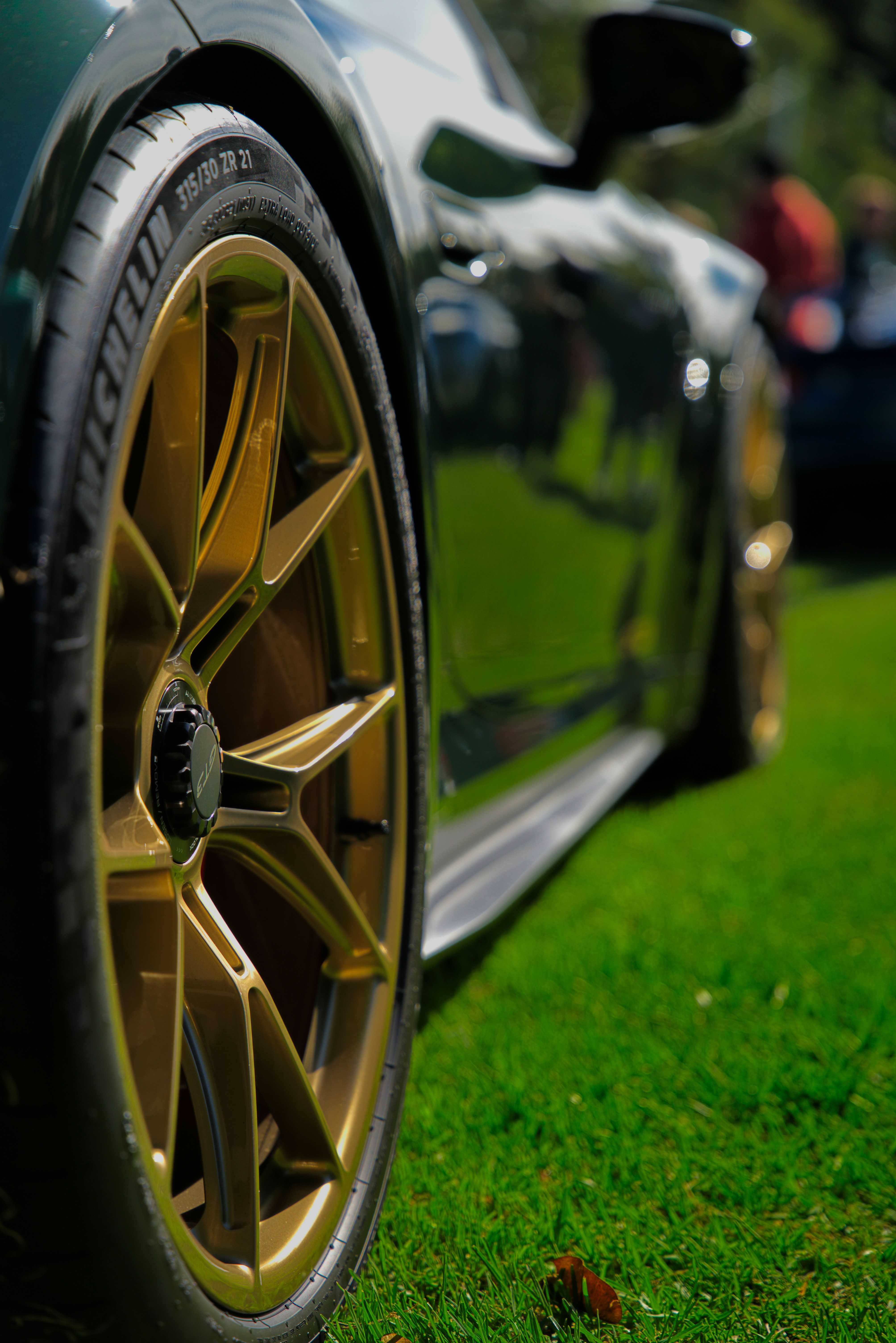 Gold spoke wheels glint at the edge of a polished green sedan