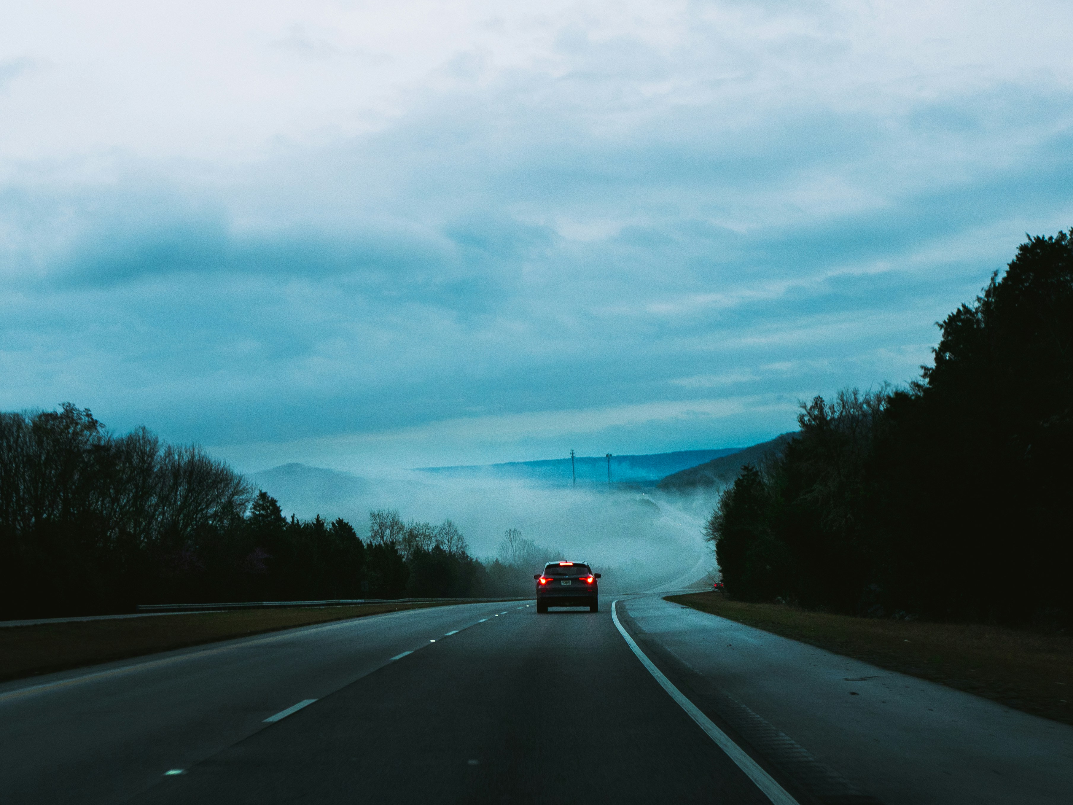 Car drives on a misty highway towards mountains.
