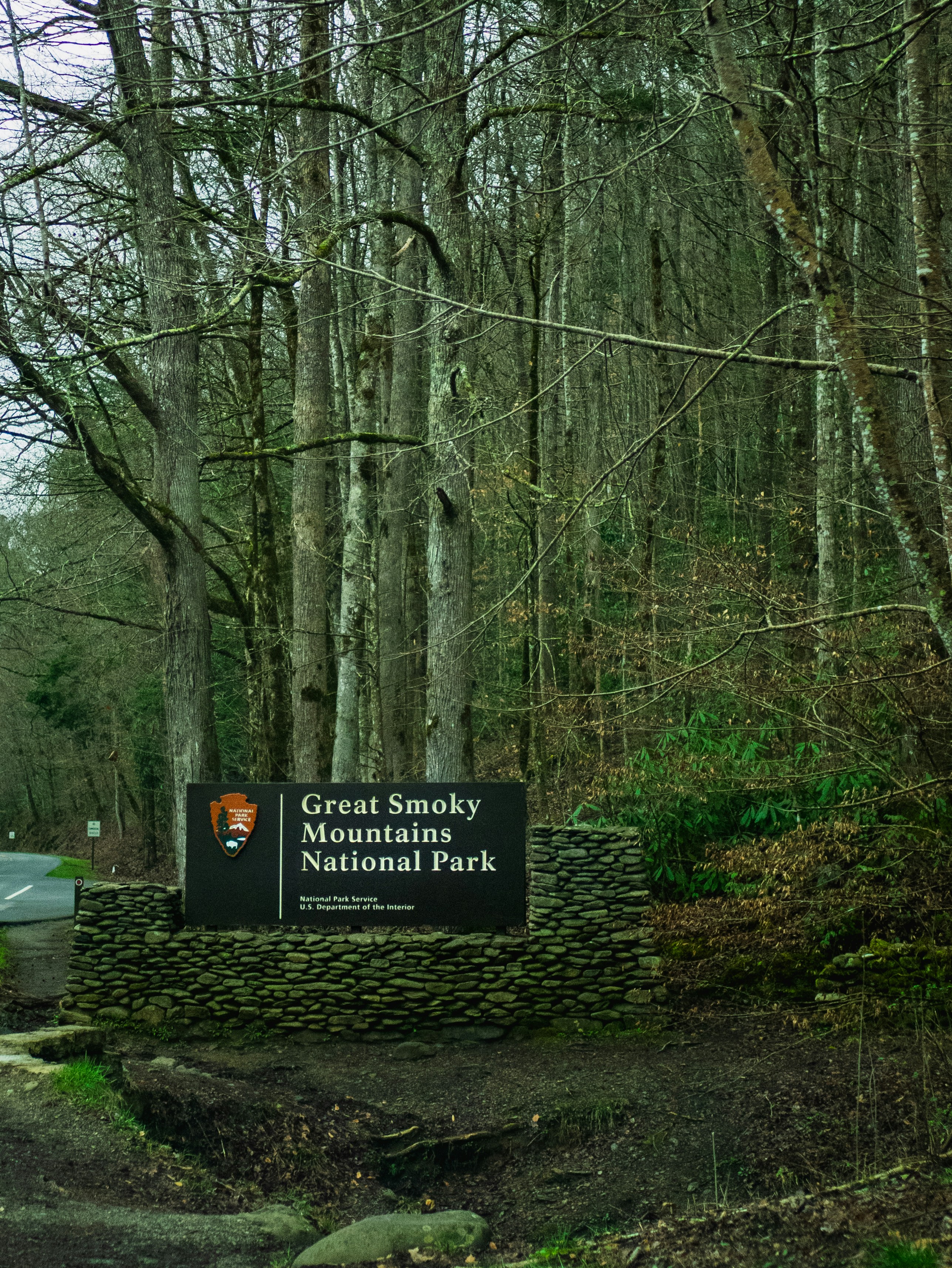 Sign for Great Smoky Mountains National Park at the forest entrance with stone base and surrounding trees.