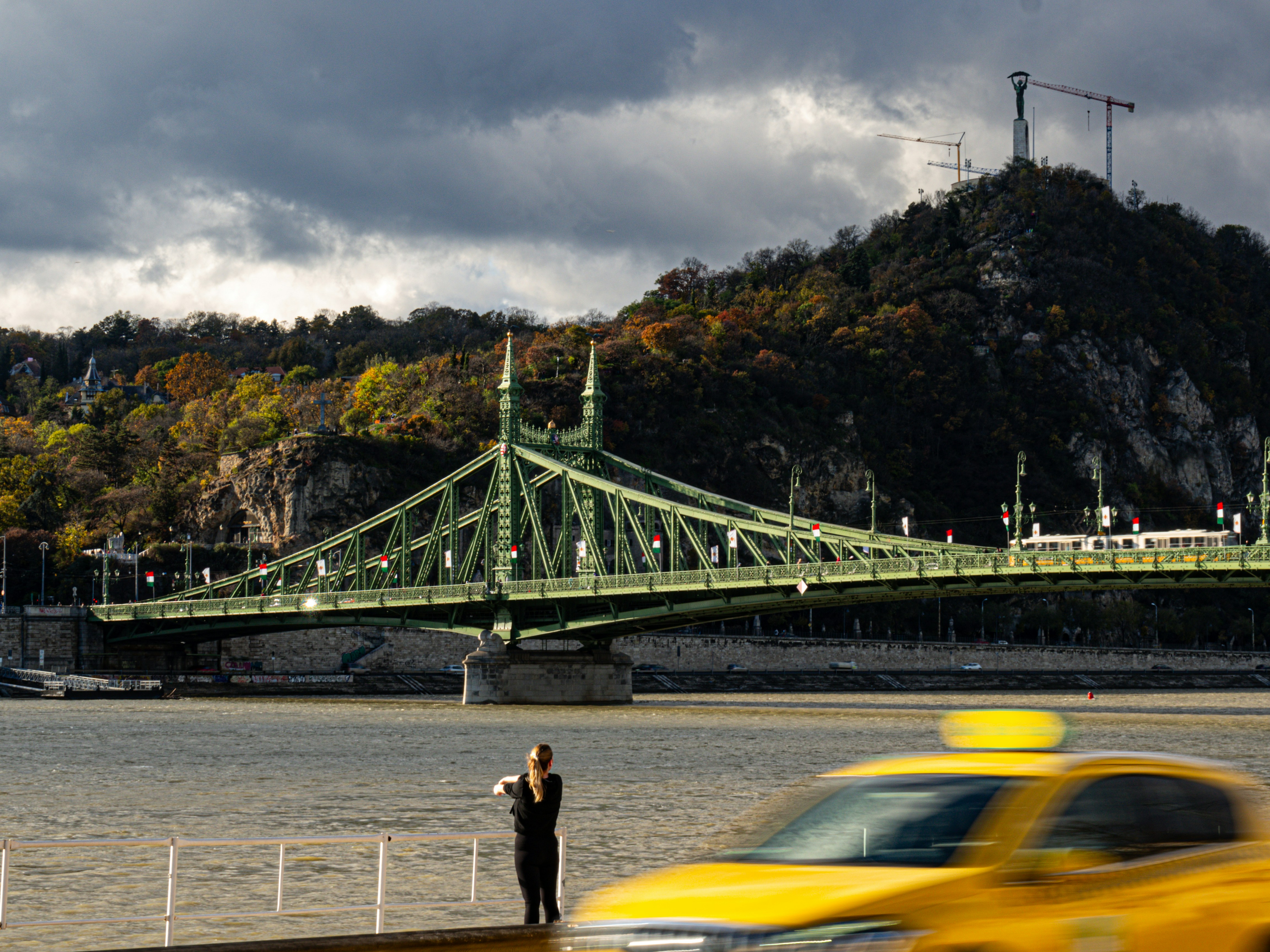 Bright Yellow Taxi in Motion by a Riverside Bridge at Dusk