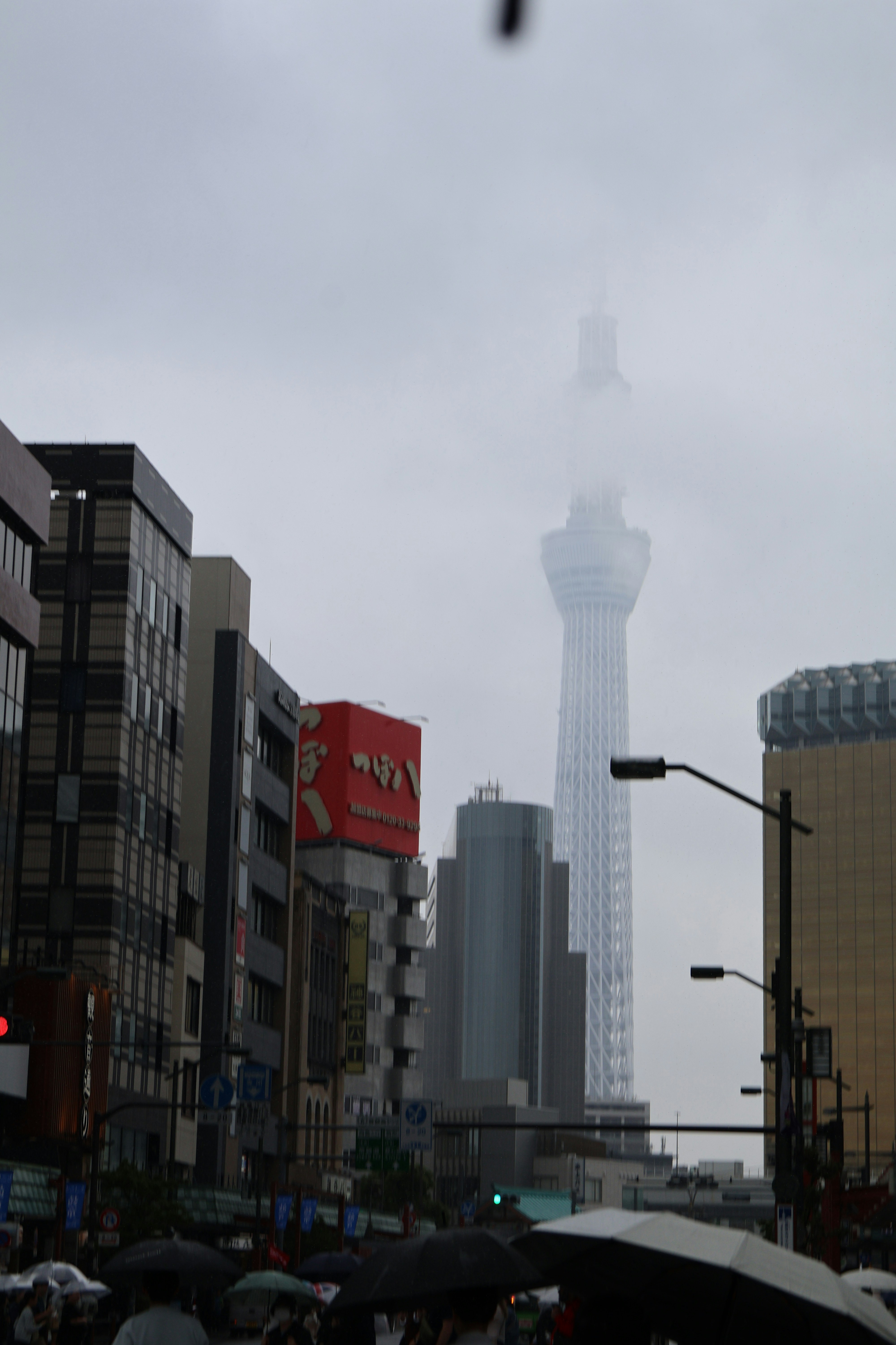Cityscape under a Misty Tower: Rain, Traffic, and a Skyward Needle