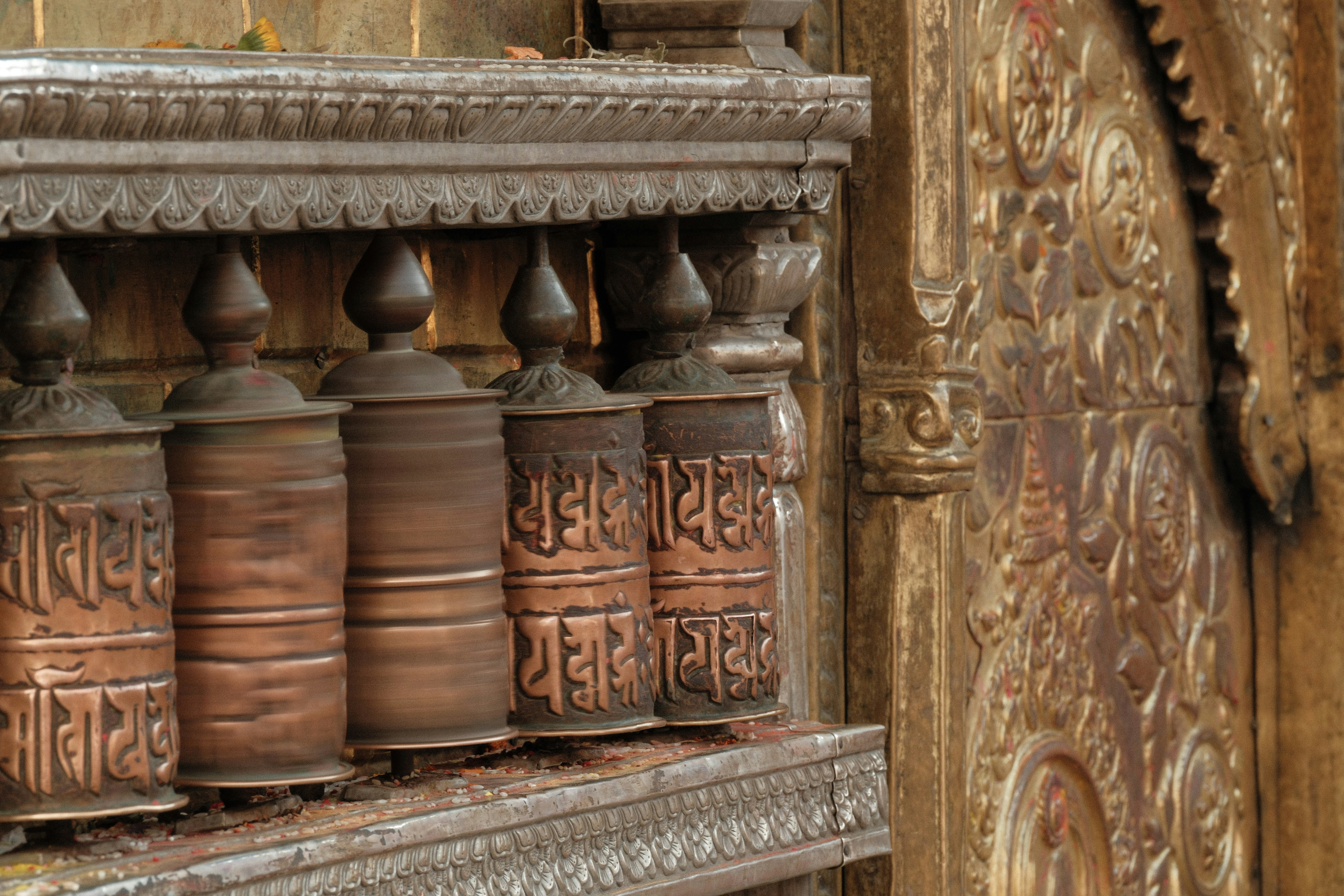 Carved prayer wheels and ornate doorway: a tactile ritual in bronze and gold