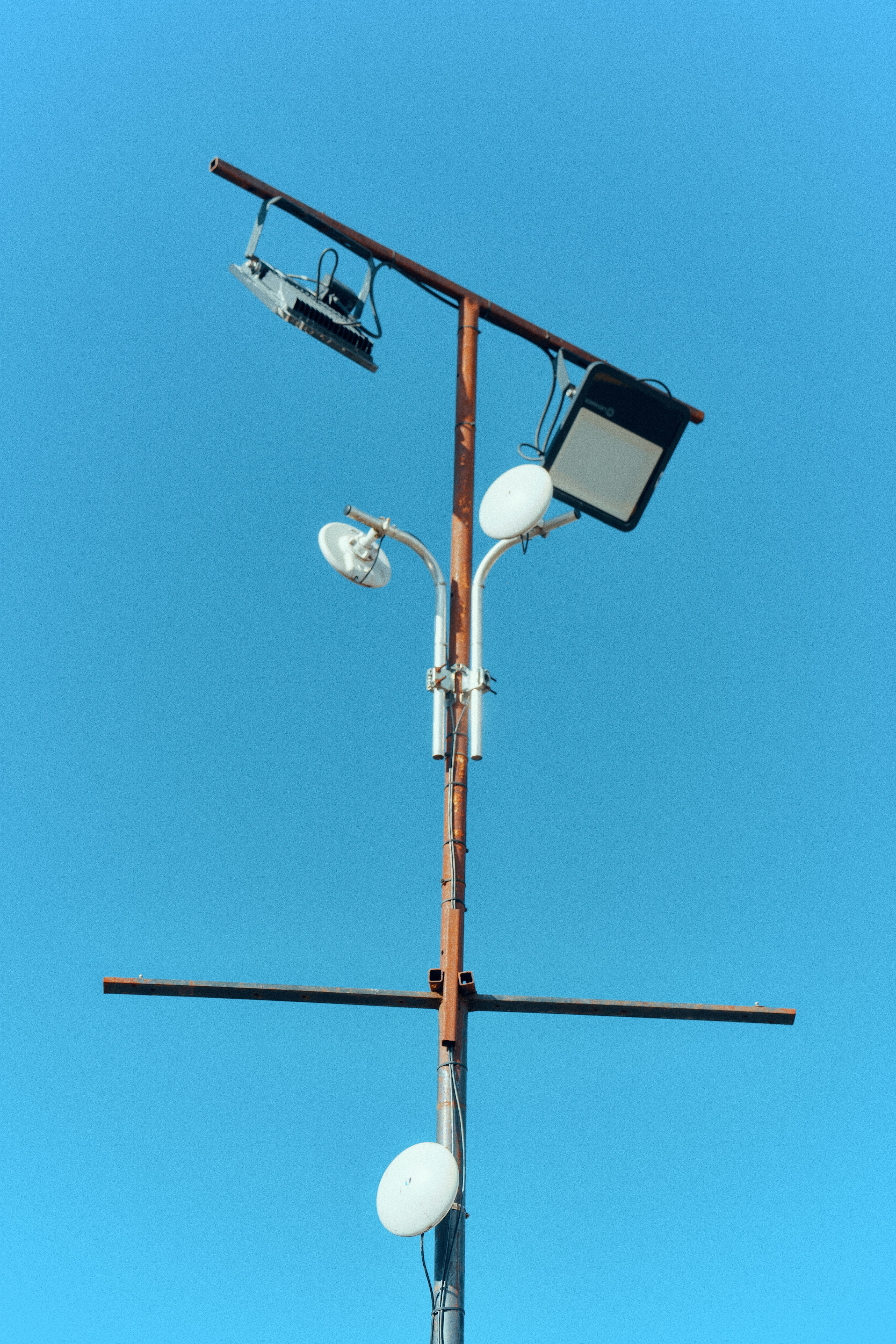 Rusty Pole with Solar Lamp and Satellite Dishes Against a Clear Sky