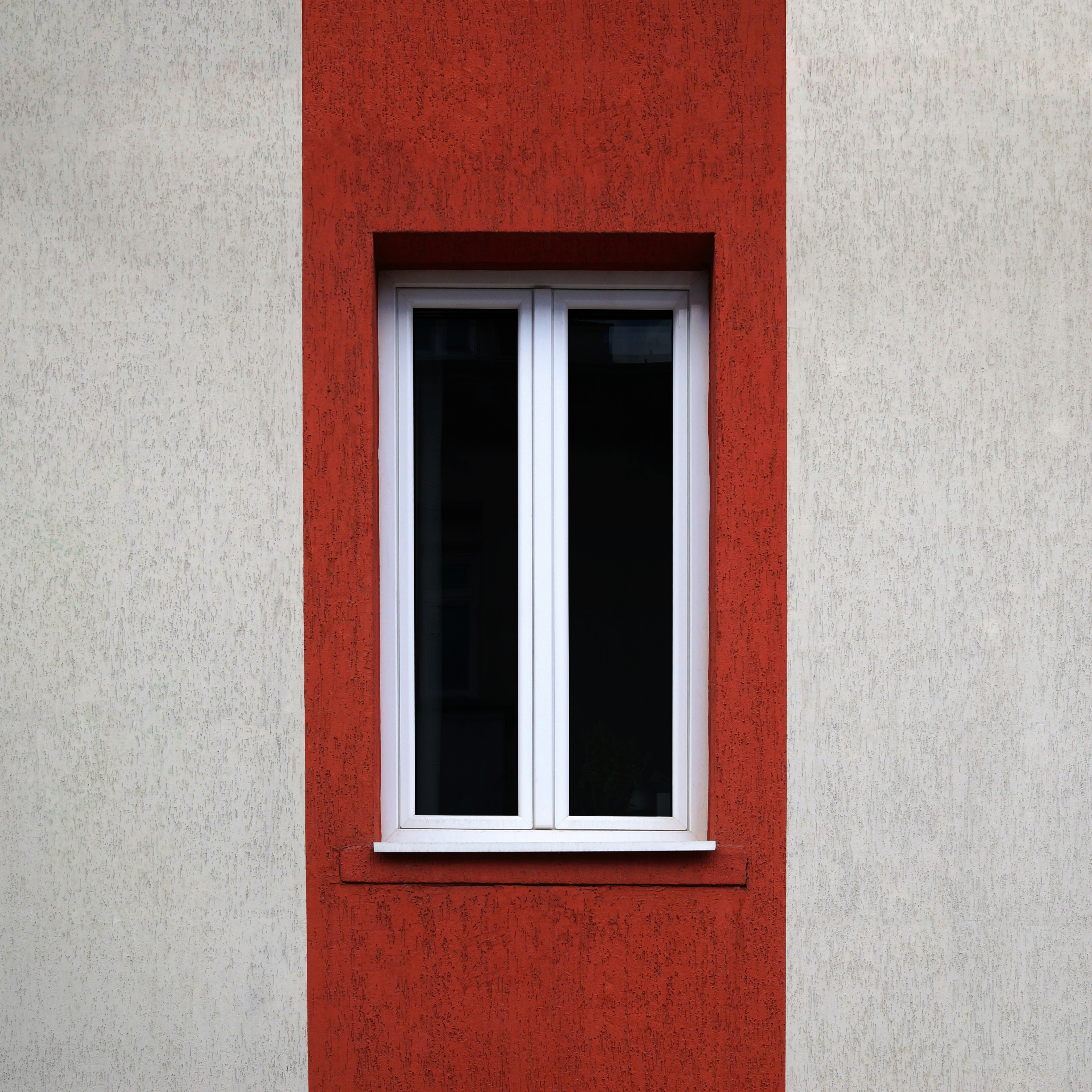 Red-framed window centered in a pale stucco wall