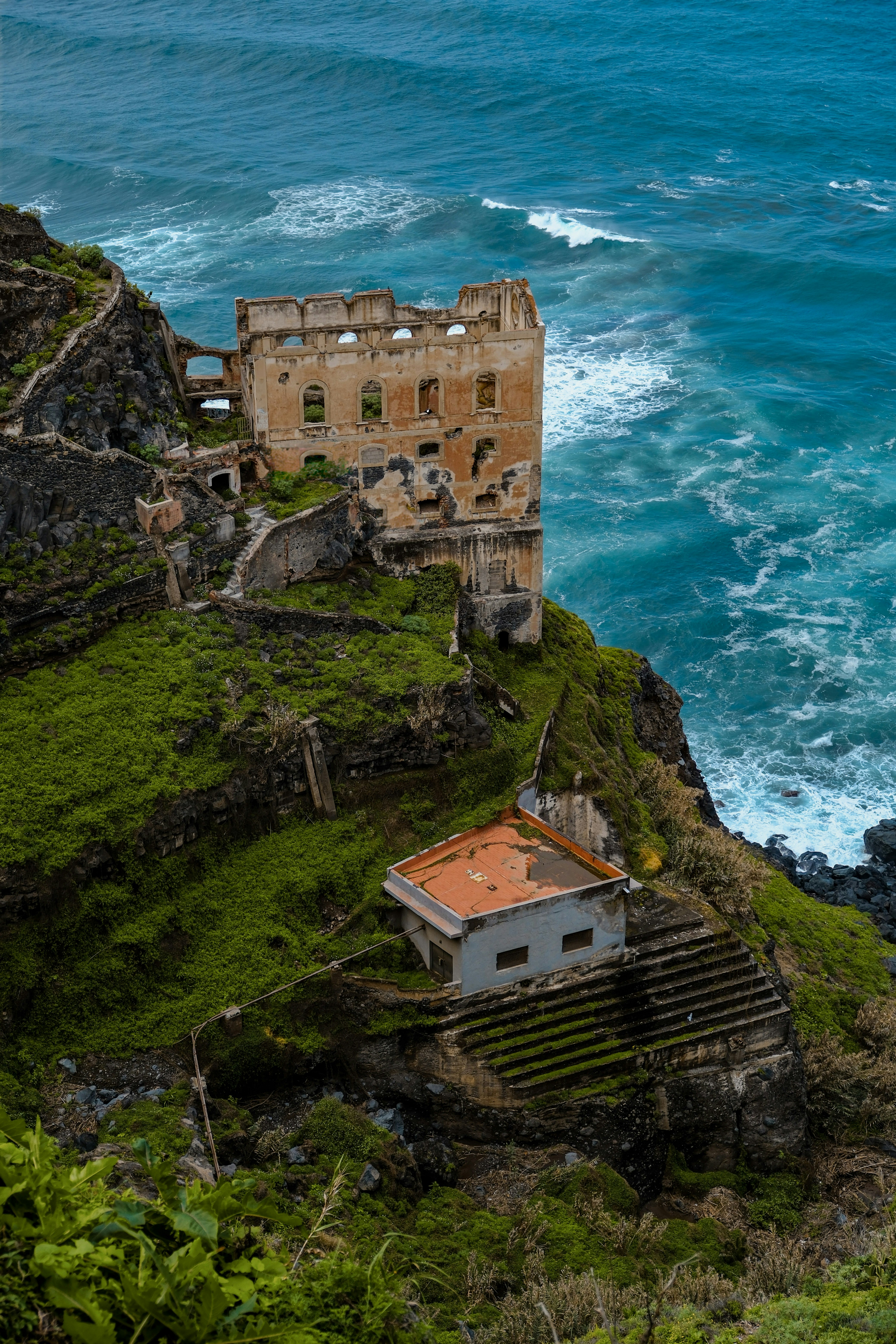Ruined fortress clinging to a cliff above turquoise sea