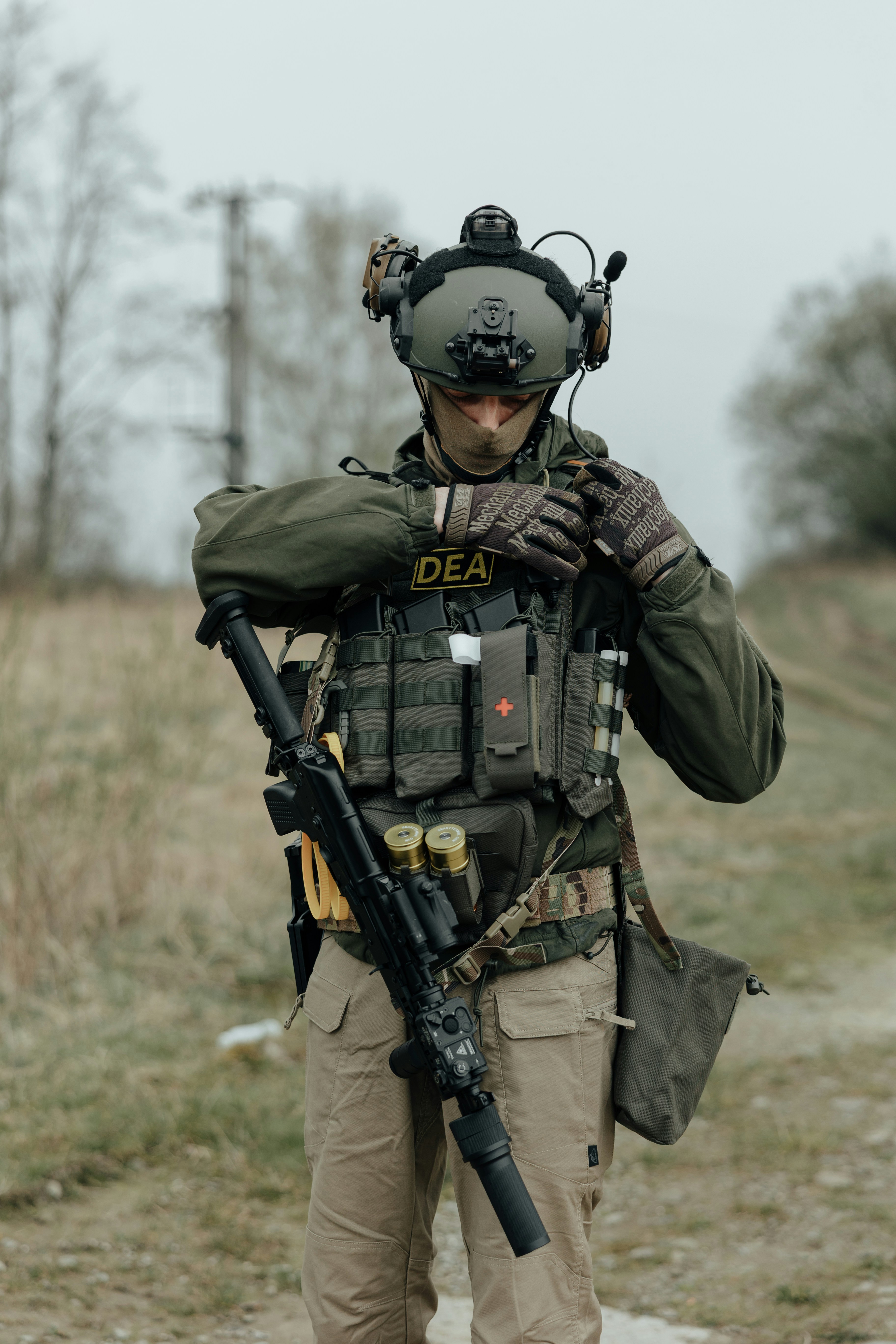 Operator in Field Gear Adjusts Comm Gear, Ready with Rifle