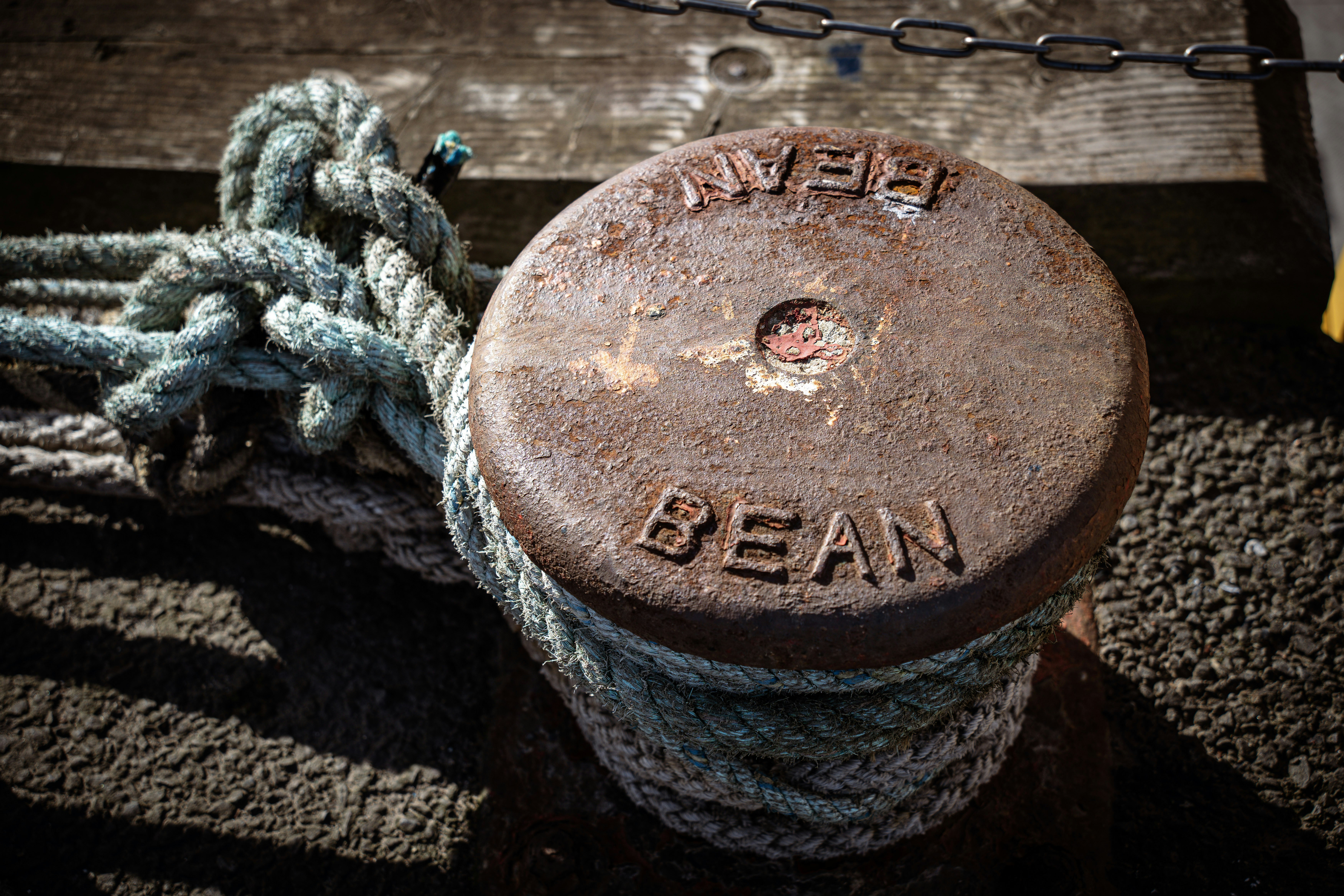 Rusted mooring weight with frayed rope in sunlit harbor deck