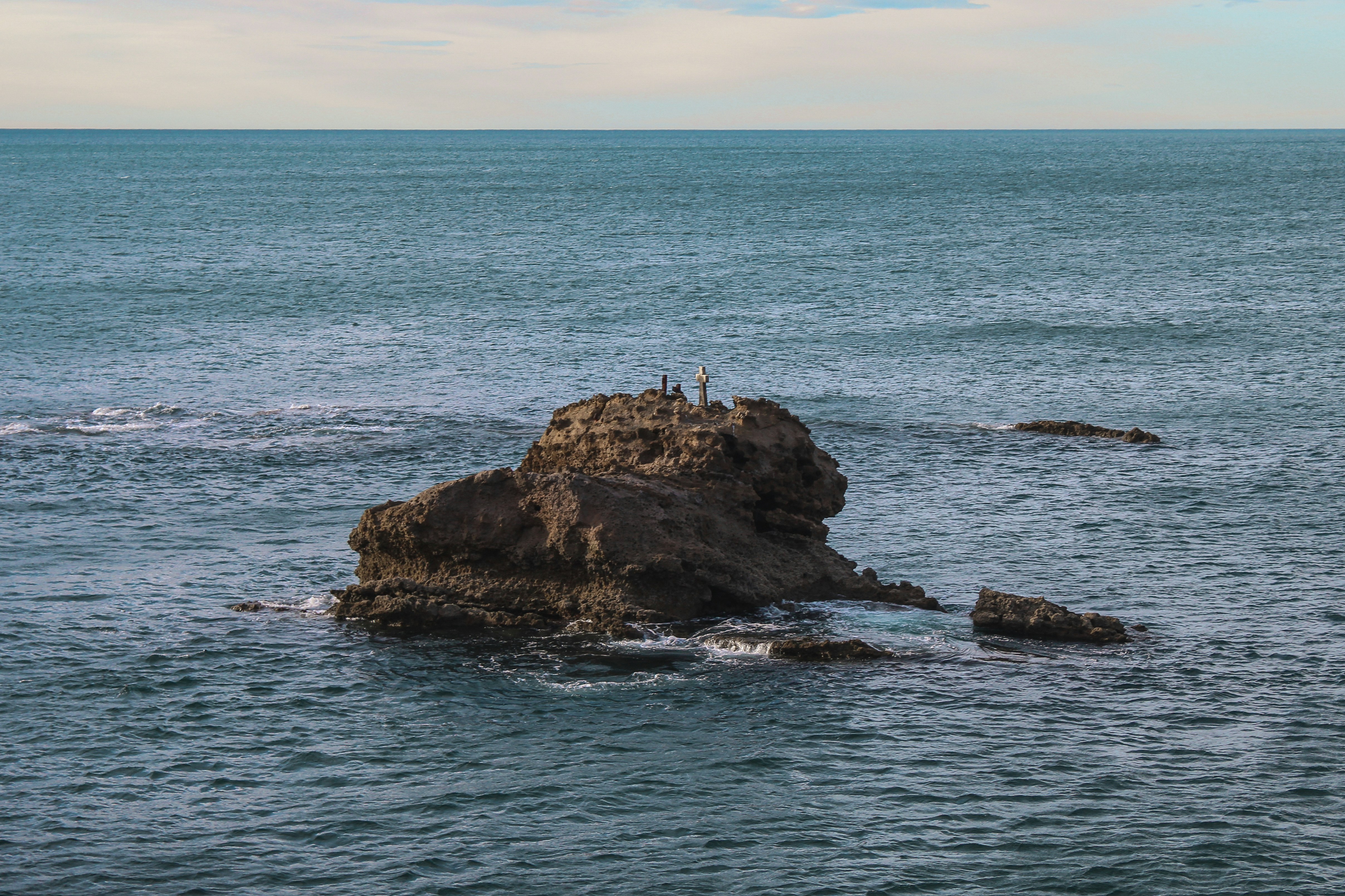 A lone rock outcrop amid a calm sea under a pale horizon
