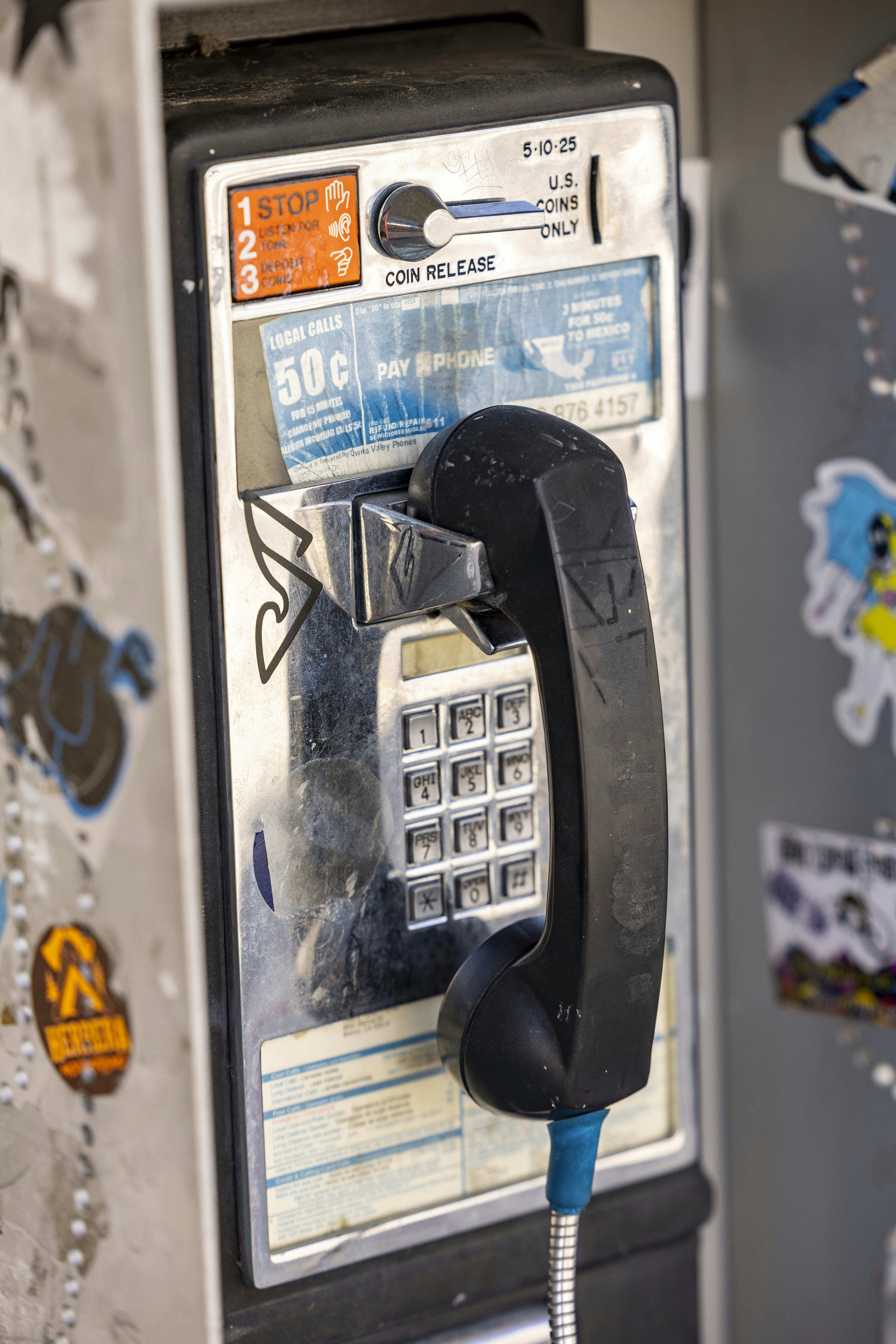 Rusted Salvation: A Payphone Oasis Amid Stickered Metal