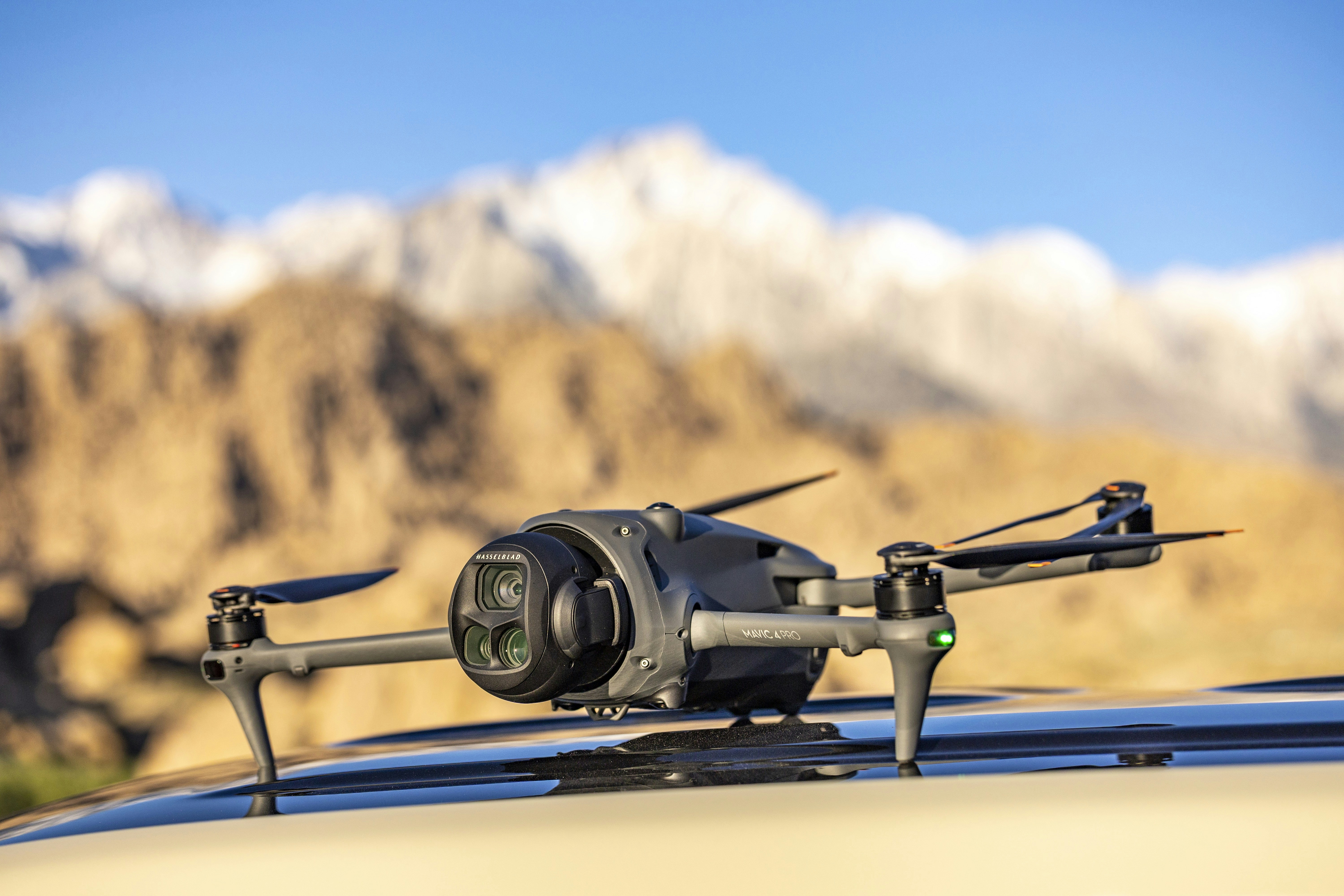 Compact drone on a car roof with a golden mountain backdrop under a clear blue sky.