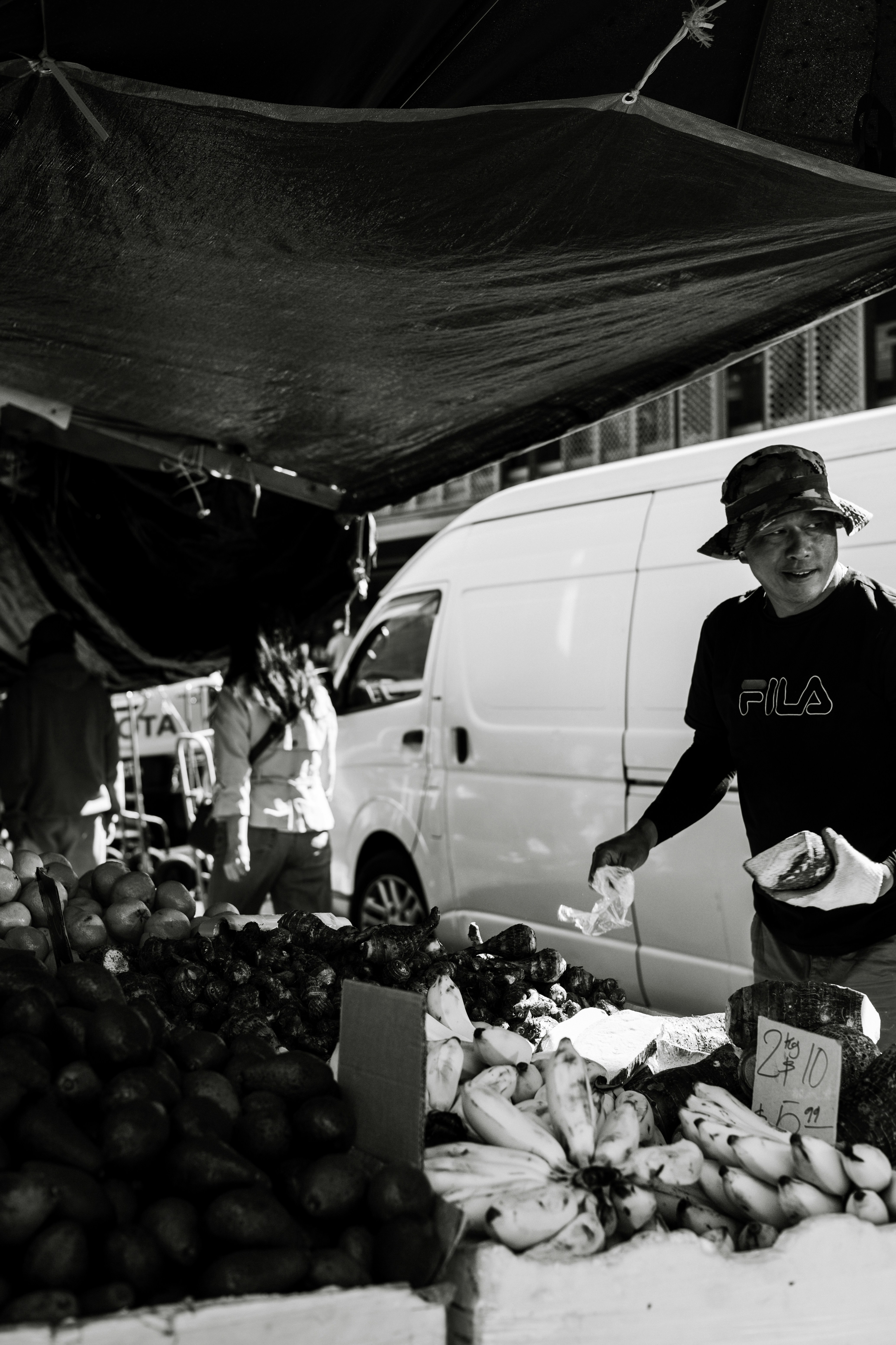 Market Vendor Under Tarp Sun, Amid Stacks of Produce and a White Van