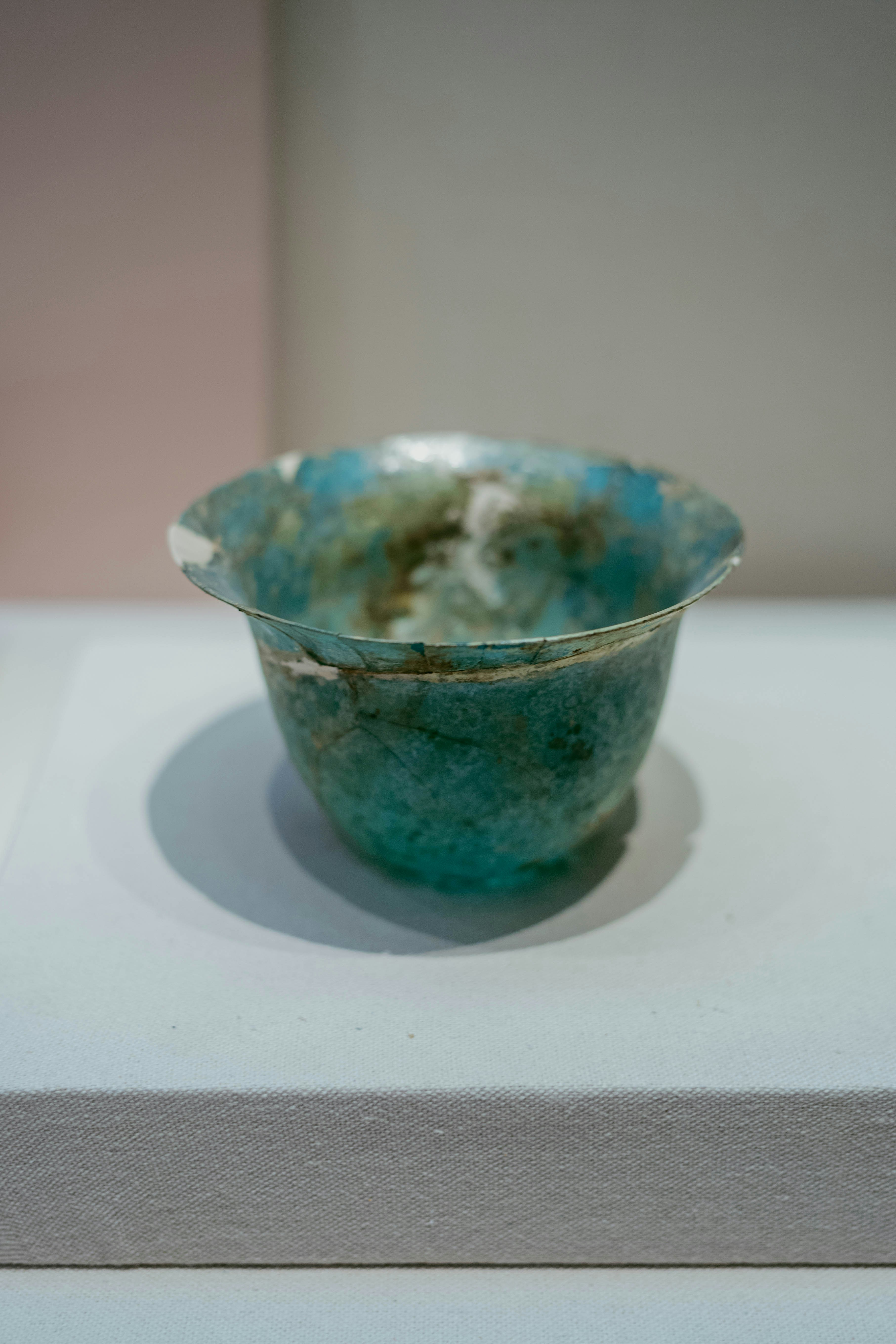 Turquoise ceramic cup on a white pedestal, softly lit gallery ambience