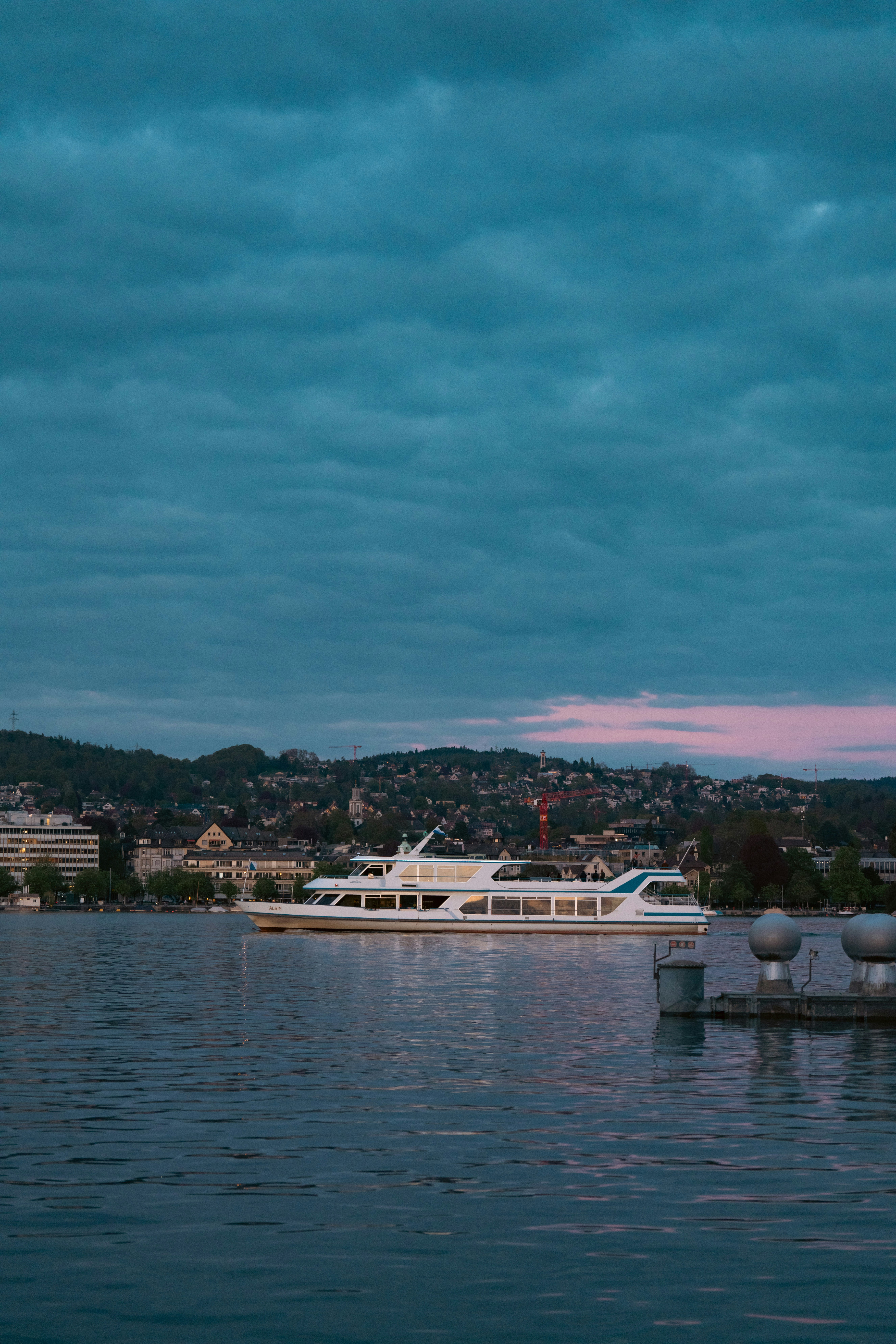 Evening Vessel: A serene lake scene with a modern passenger boat gliding past the city lights