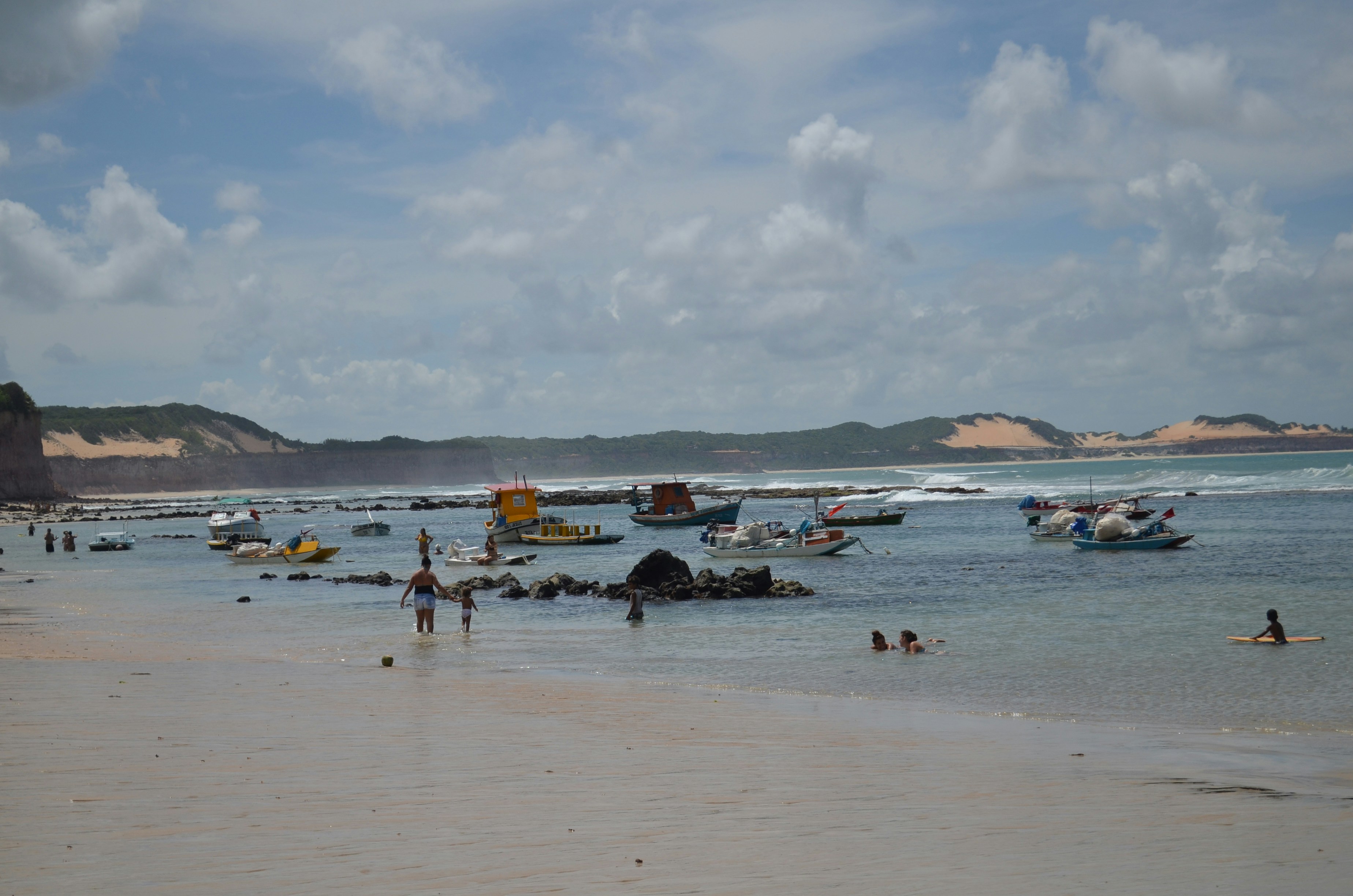 Sunlit Shore: Boats Rest at the Tide as Beachgoers Cool Off