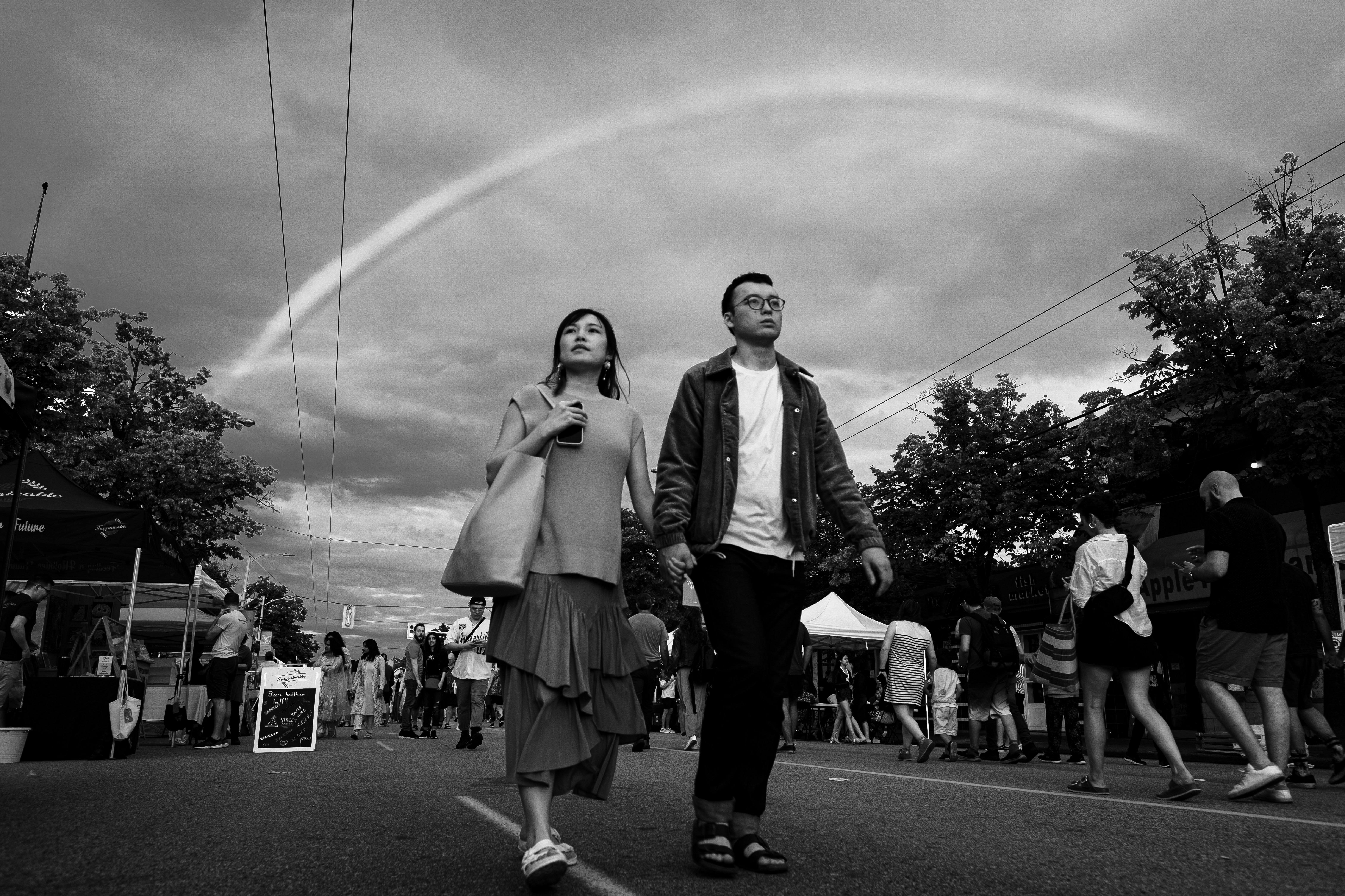 Two Stride Through a Rainbow Arc: People Walk Under a Street Fair Sky