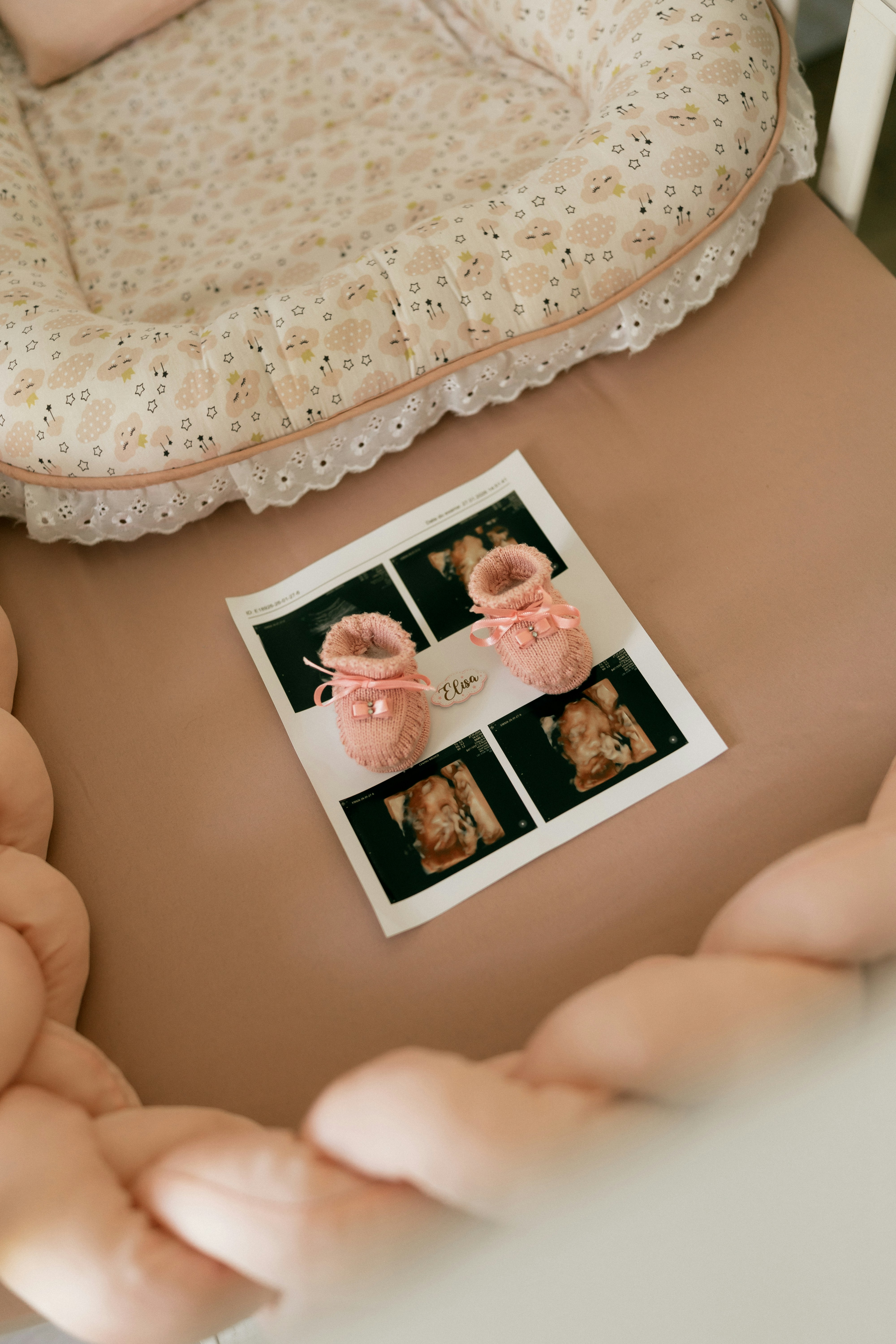 Baby shoes rest on a plush cream surface beside a flower-patterned baby nest