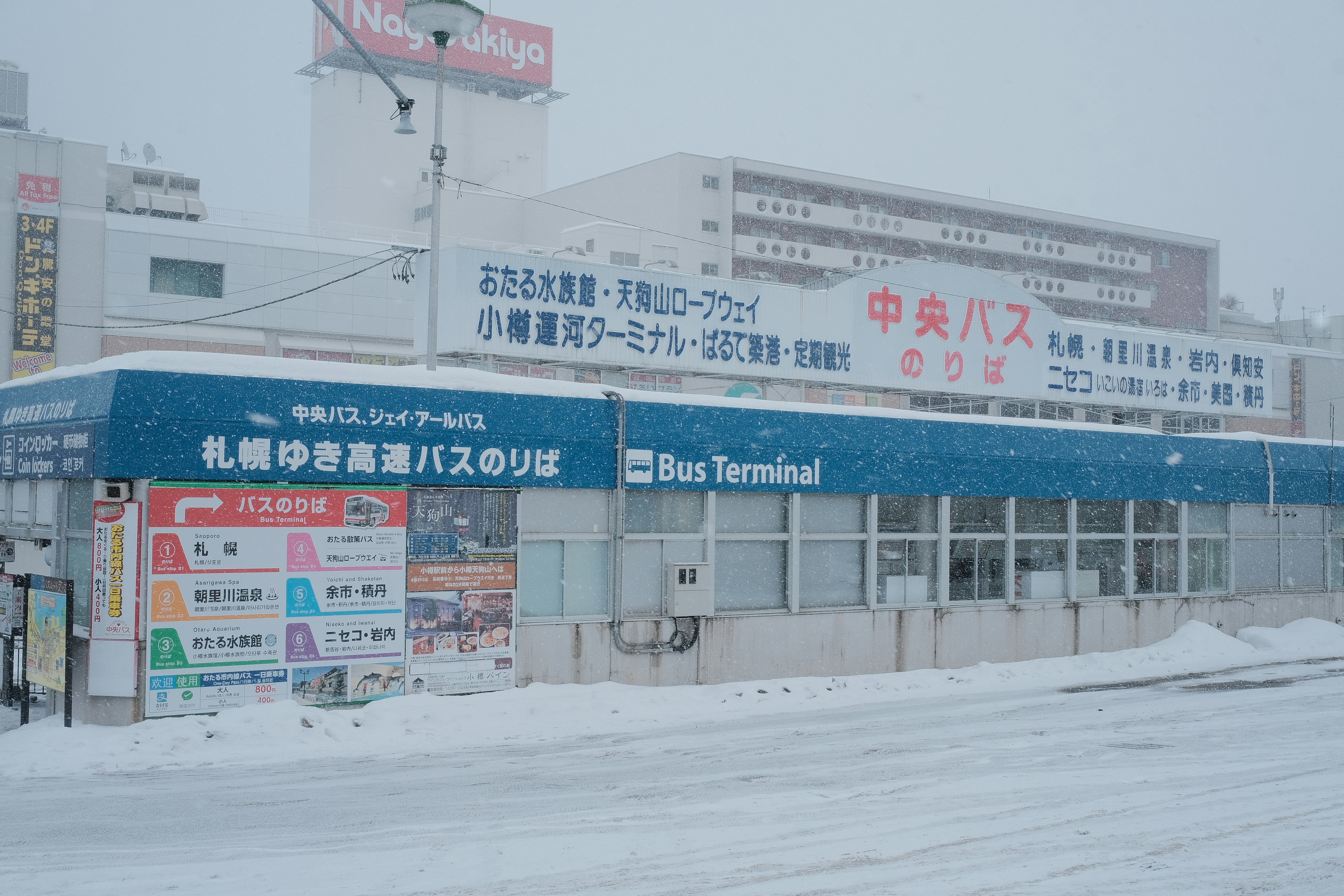 Bus terminal covered in snow with blue signage and a snow-dusted platform, suggesting calm winter weather and quiet transit activity.