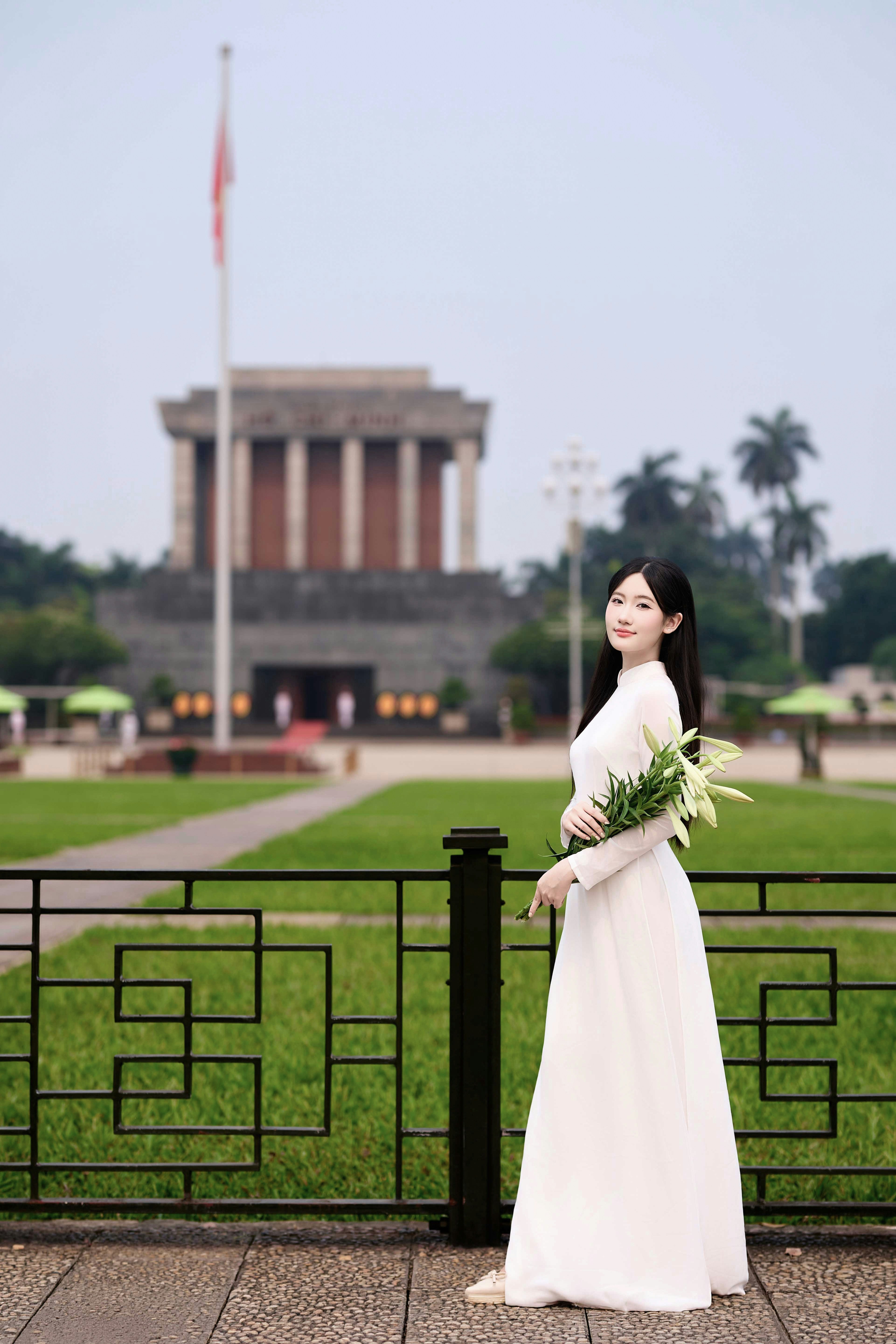 White dress, green lawn, and distant monument: a poised portrait by the rail