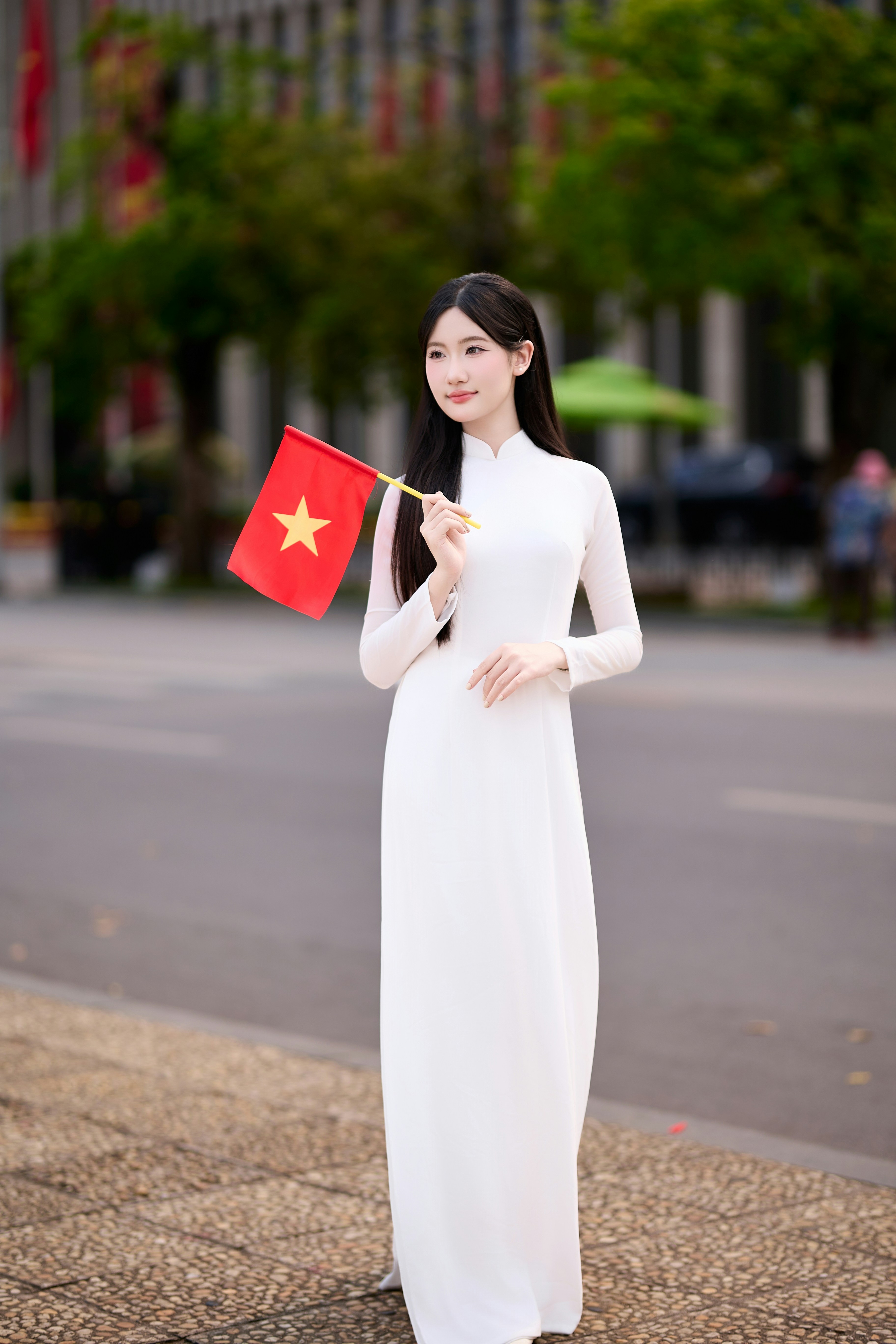 Flag Bearer in White Ao Dai Standing Beside a City Street