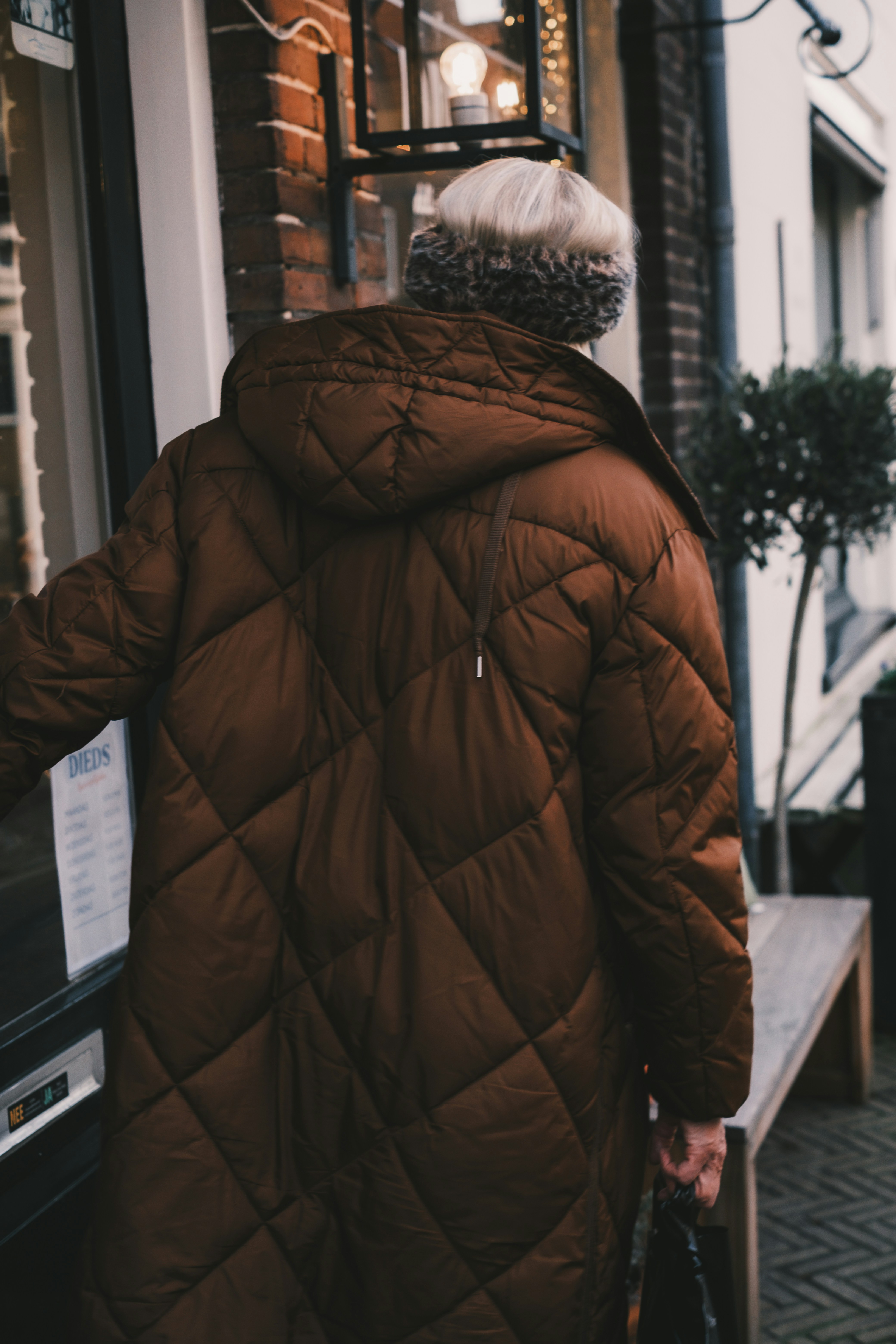 Warm silhouette: a person in a quilted brown coat stepping through a cozy street scene