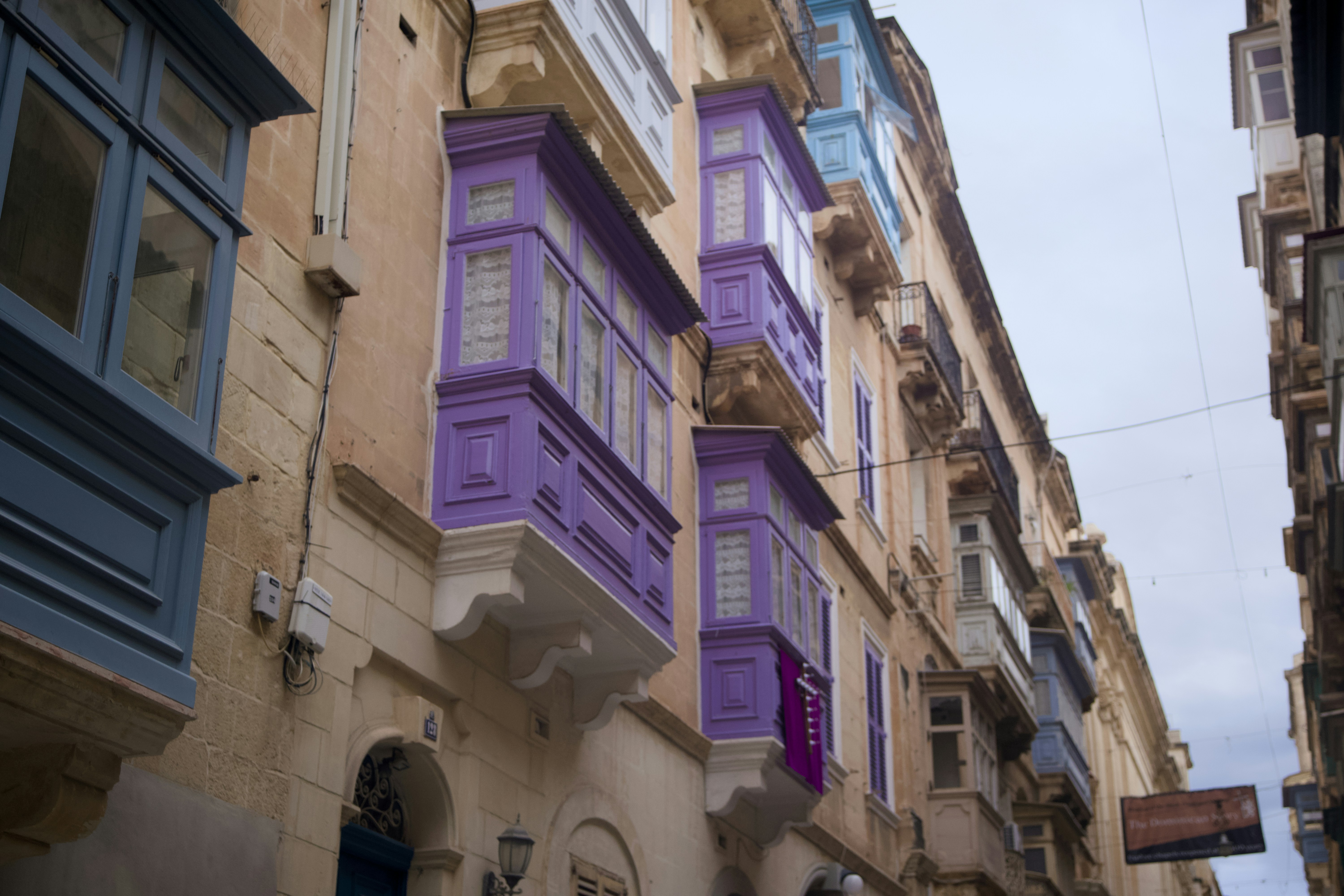 Purple balconies overlook sunlit limestone street