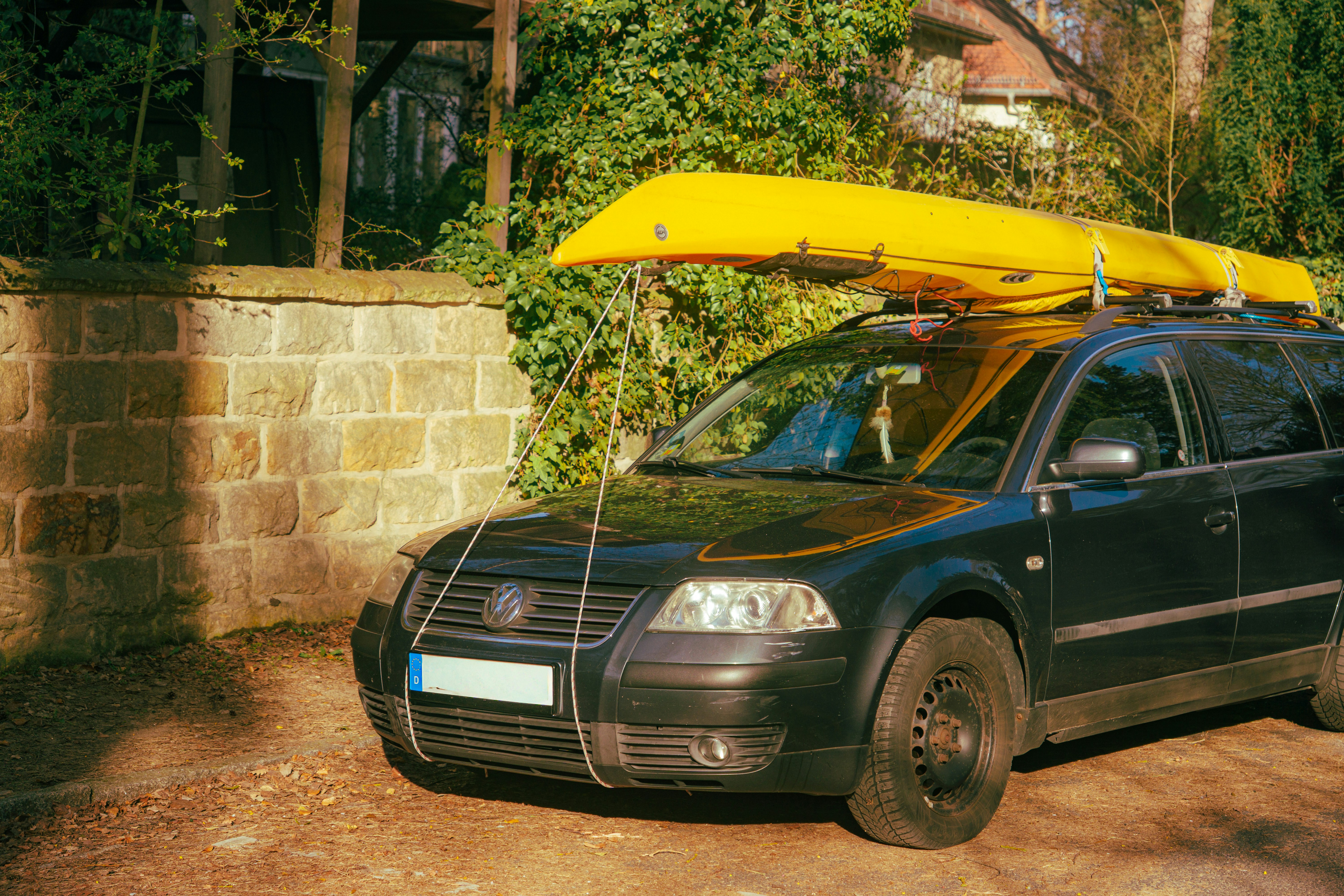 Yellow Kayak on a Dark Blue Family Wagon Resting by the Fence