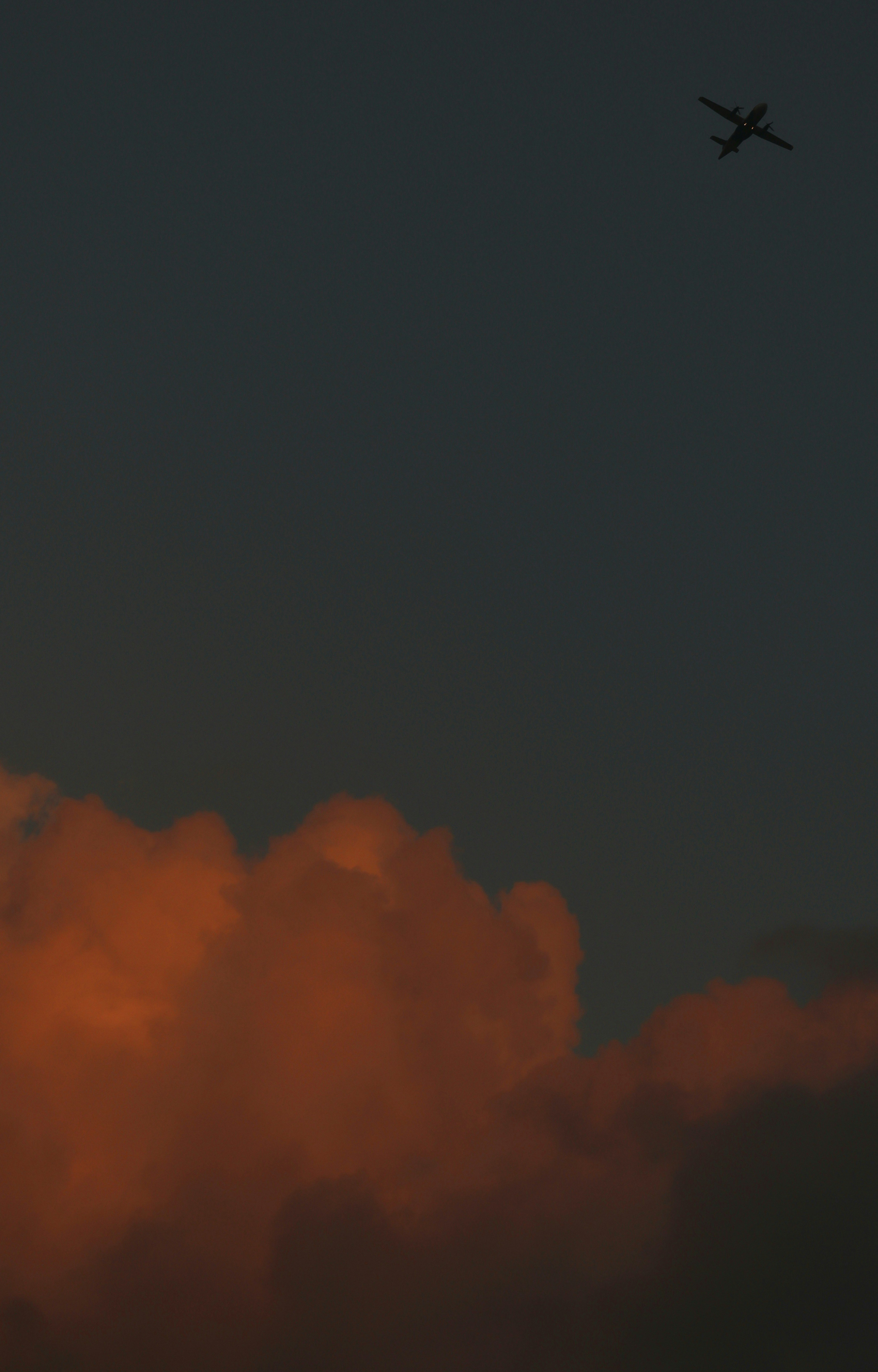 Plane Silhouette Above Ember Clouds at Dusk