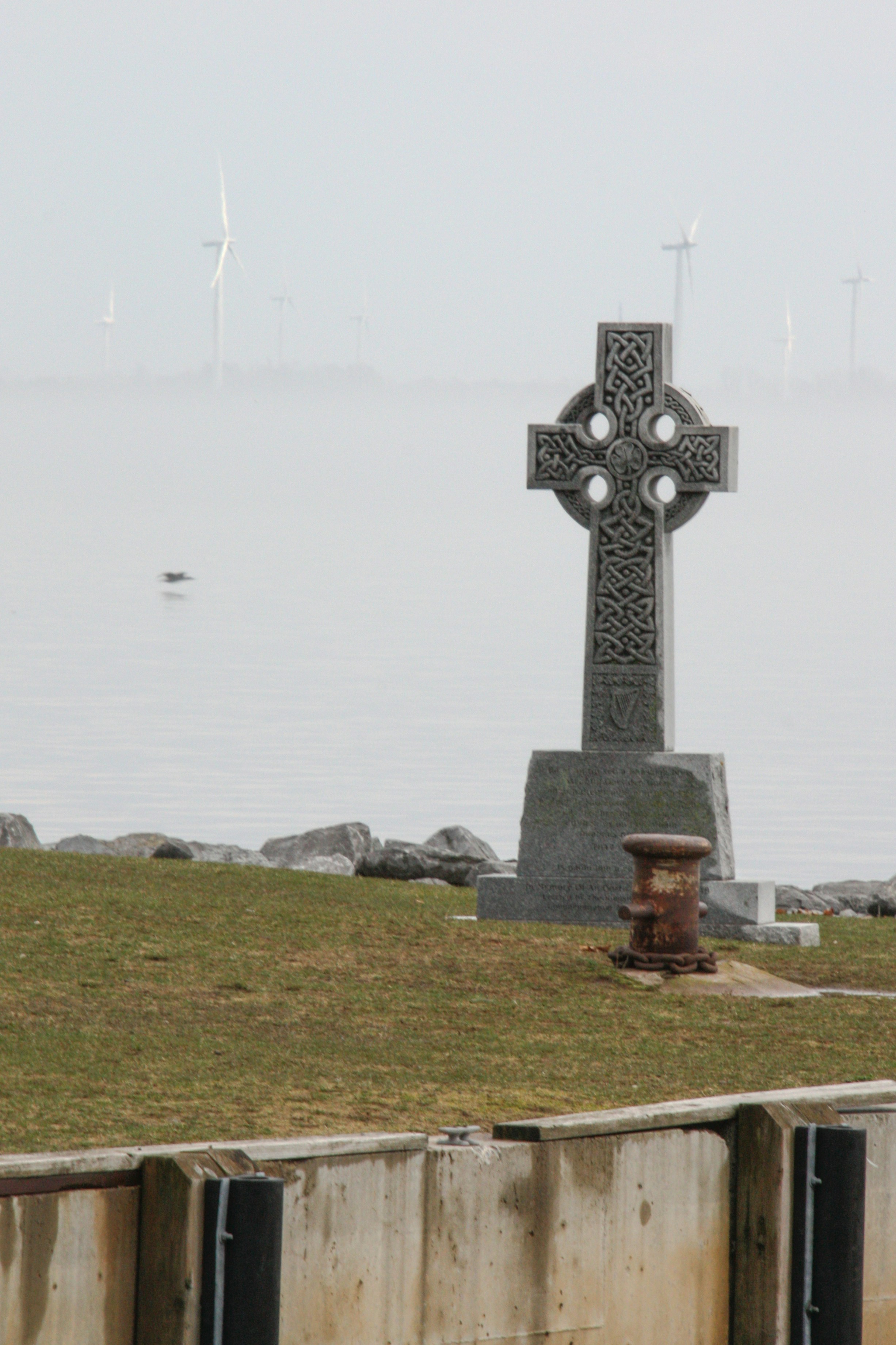 Windmill silhouettes beyond a Celtic cross by the lakeside