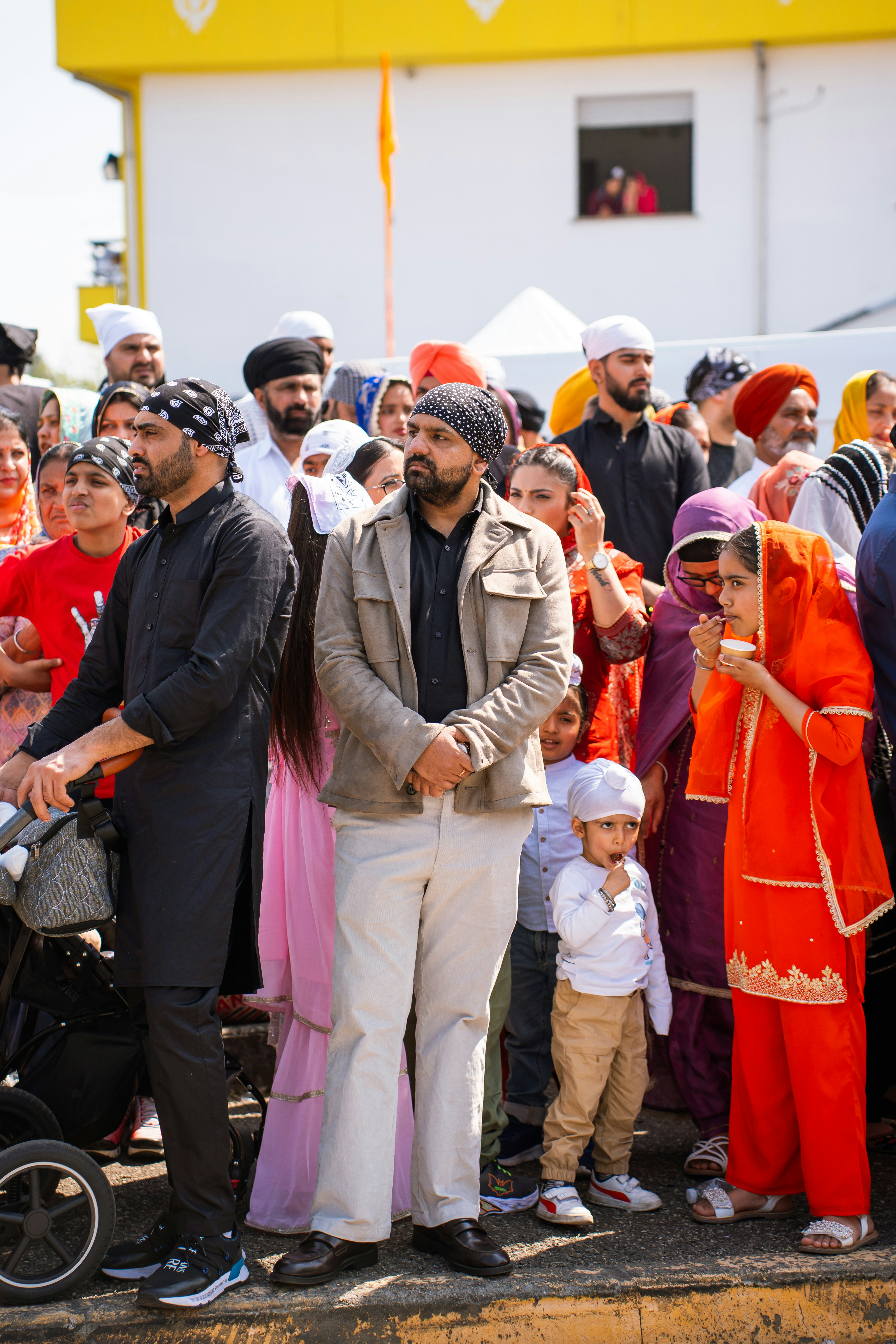 Crowd in vibrant traditional attire gathers outside a bright yellow building