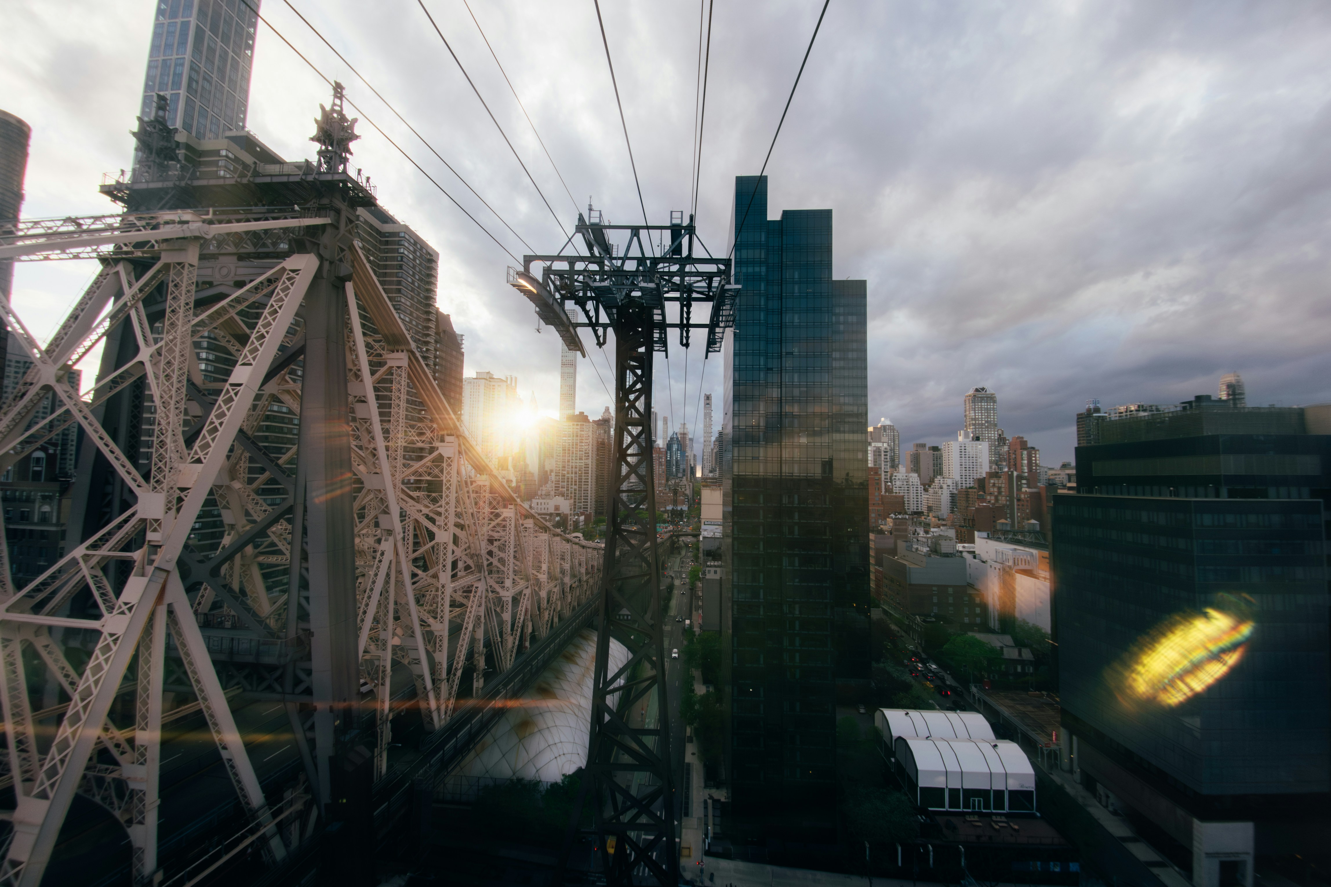 Urban skyline and steel bridge towers recede into a sunburst overcast cityscape, with high-tension cables and a reflective glass building commanding the frame.