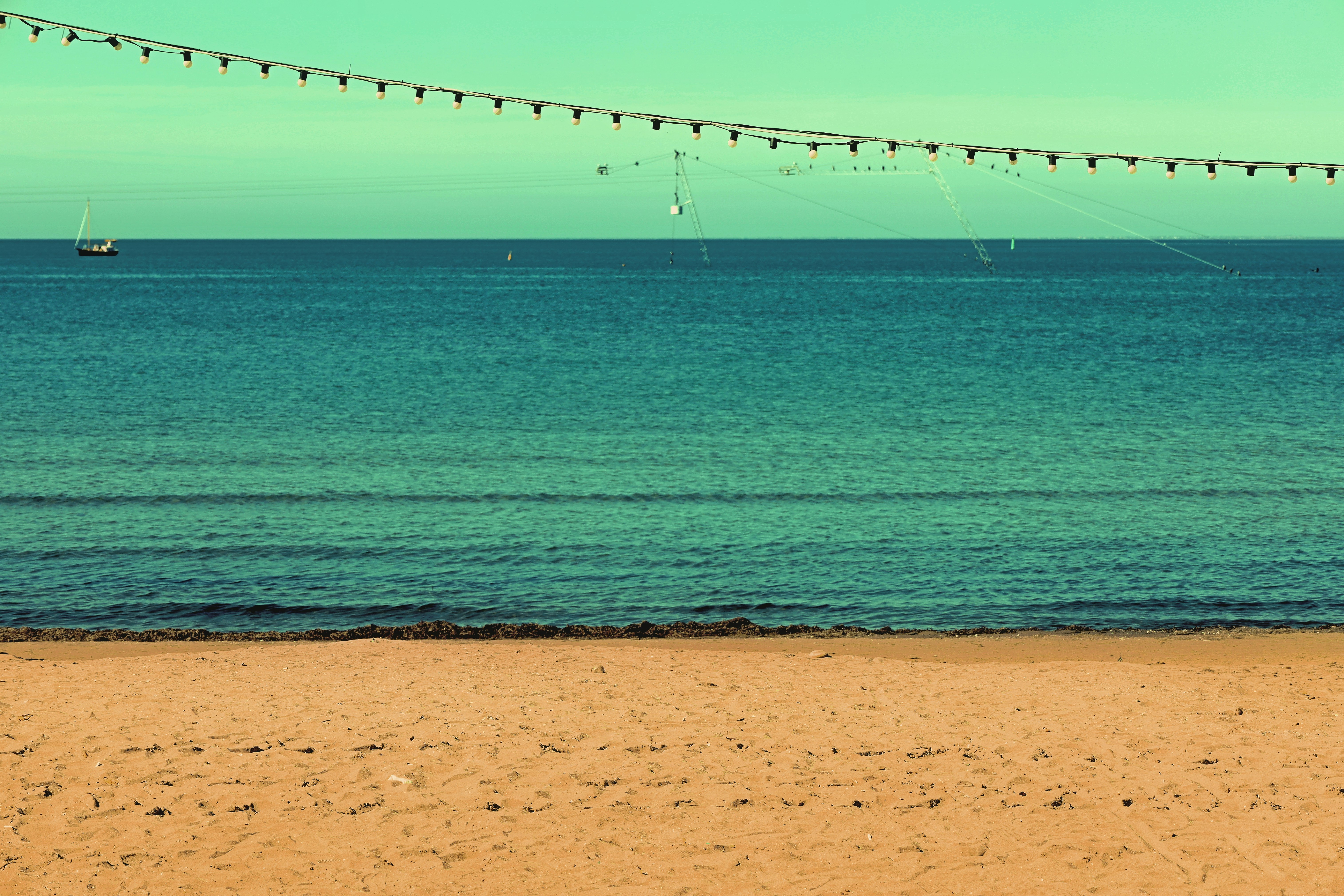 Sunlit Beachscape with Distant Sailboats and Decorative Lights